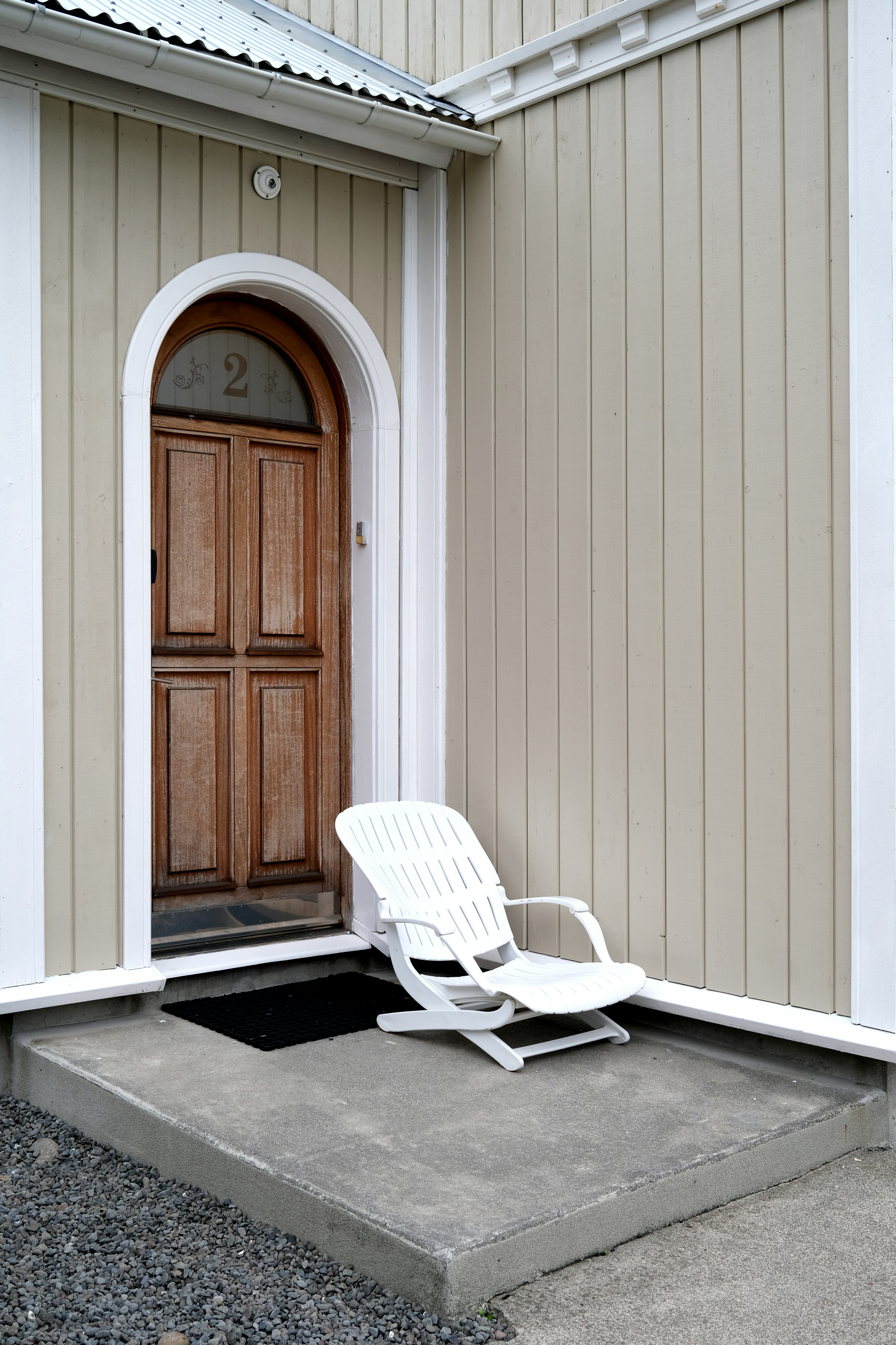 Quiet Archway: Weathered Door Framed by Beige Siding with a White Chair
