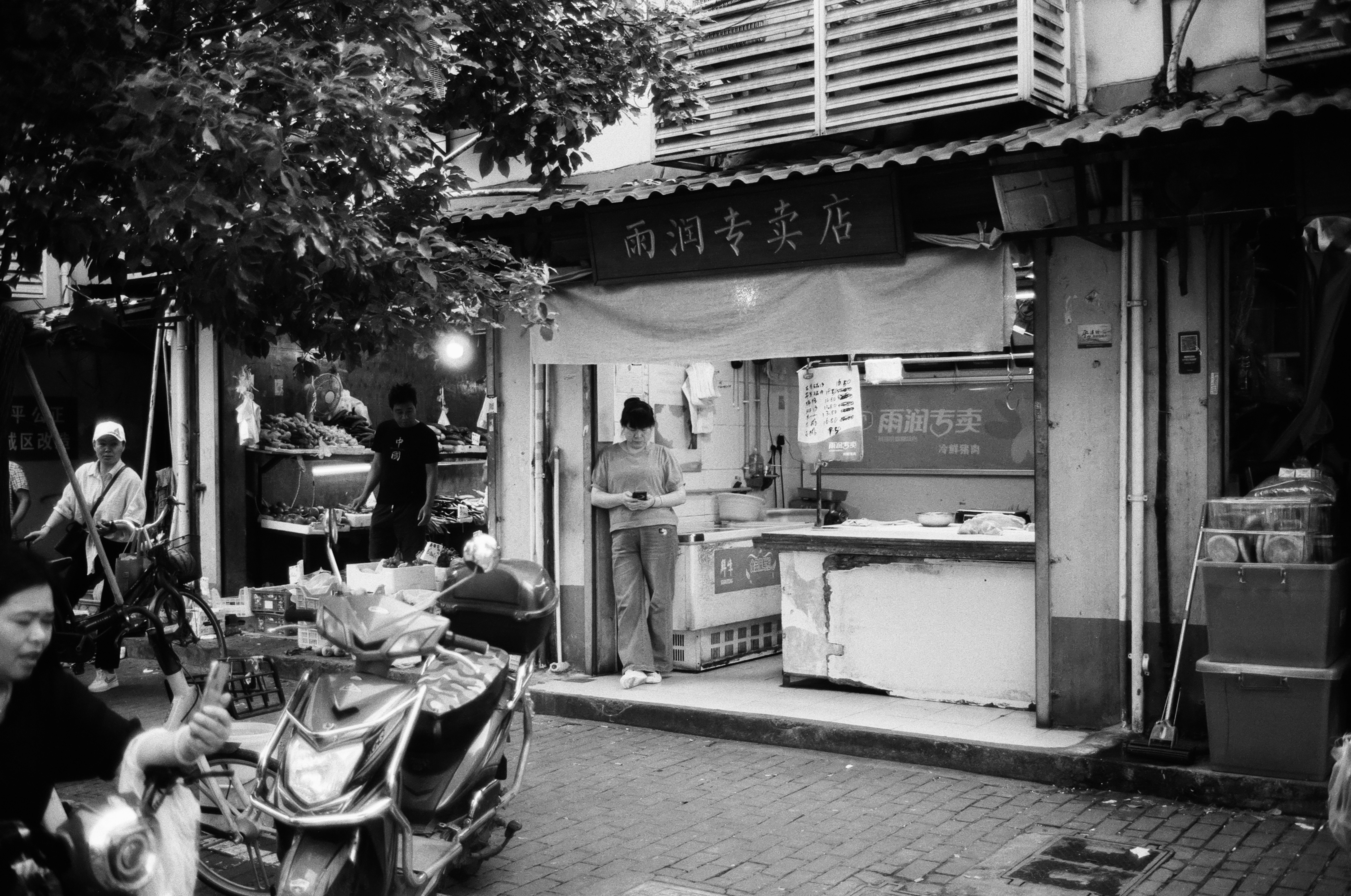 A bustling street scene featuring a local eatery with a vendor preparing food, surrounded by the vibrant energy of the market. The monochrome tones enhance the nostalgic atmosphere.