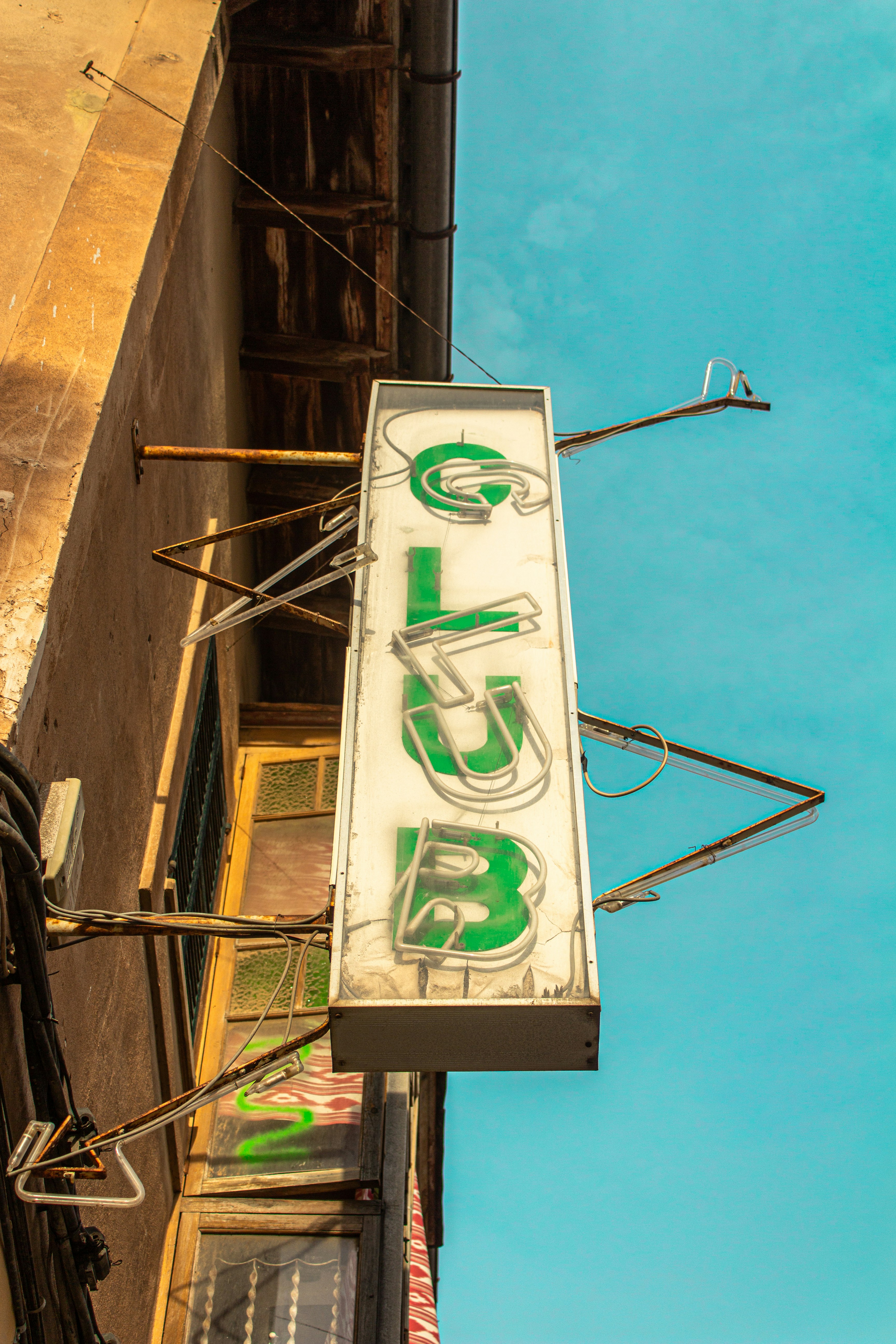 Illuminated vintage club sign hanging against a bright blue sky, showcasing a blend of retro design and urban charm.