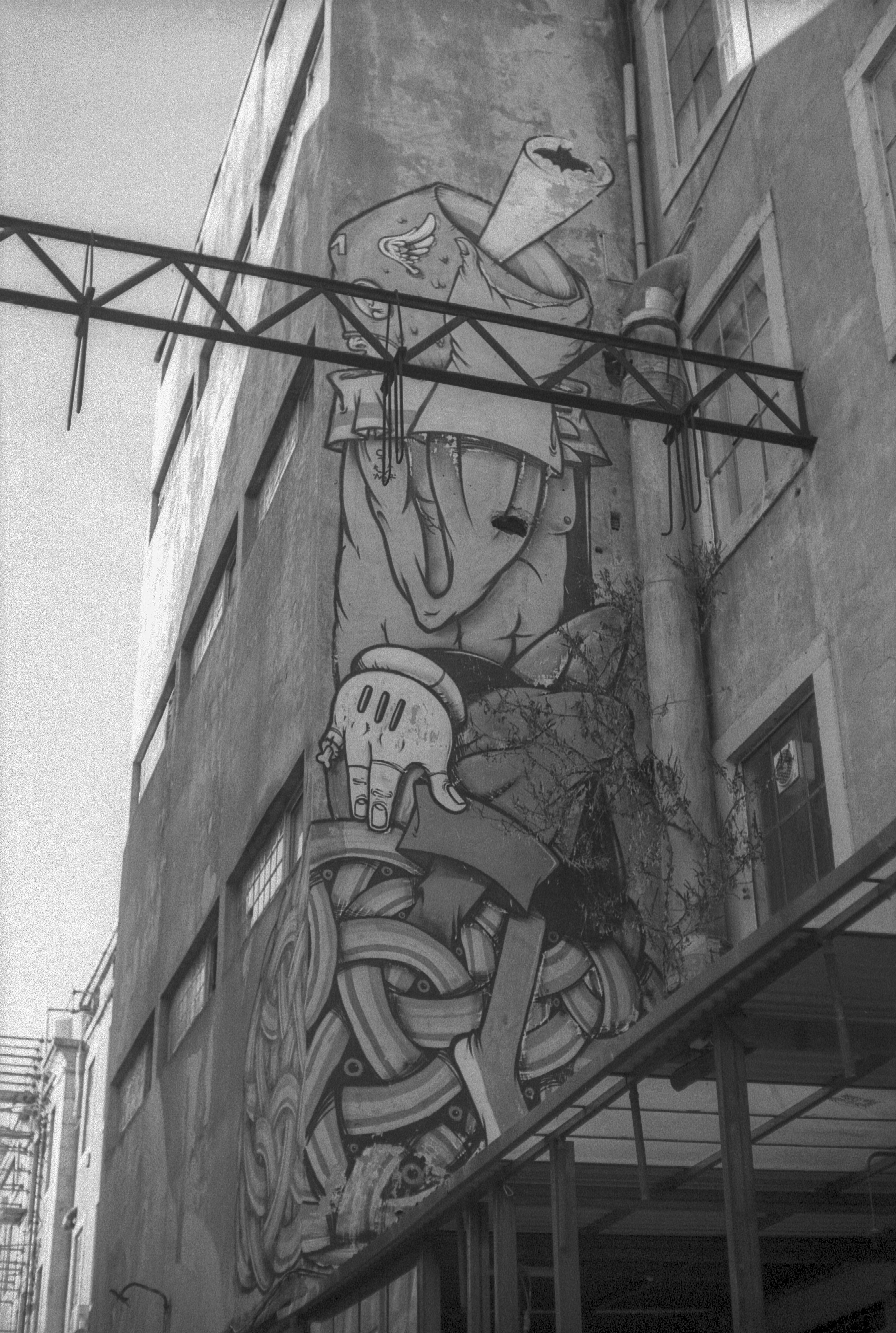 Monochrome graffiti mural on a brick wall depicts a surreal figure with a top hat and skeletal elements, an illustration in urban art.