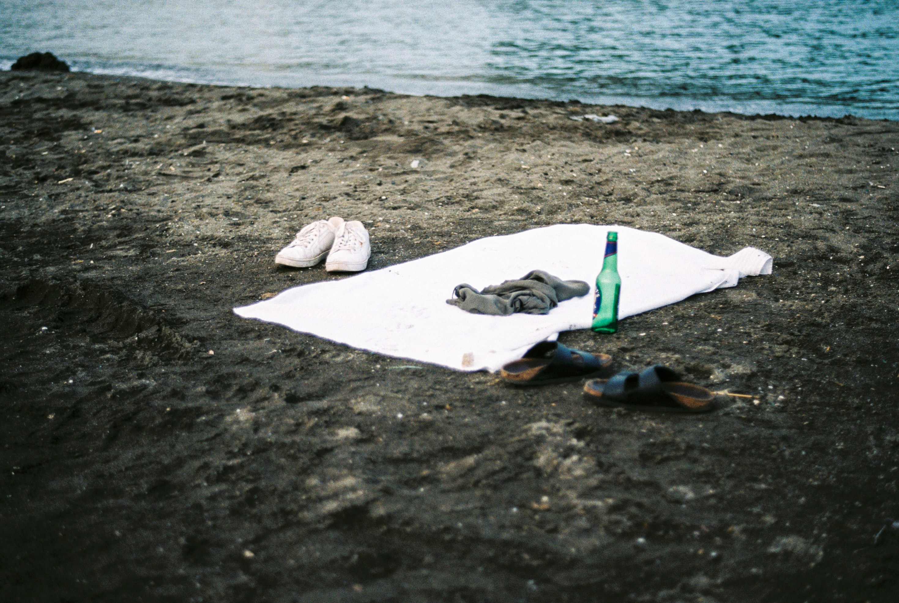 Seaside Pause: White Towel, Green Bottle, and Footwear on a Quiet Pebble Shore