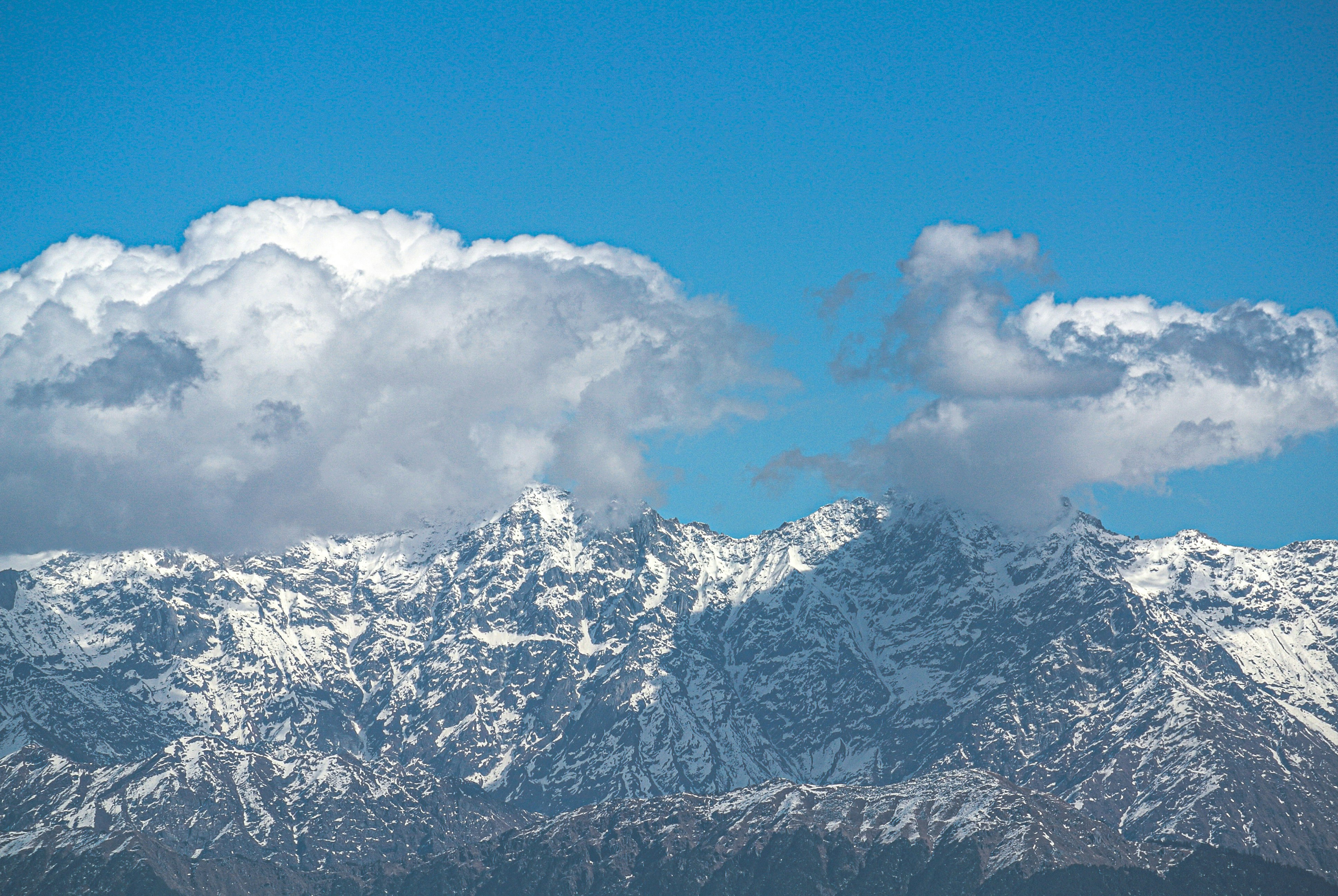 Snow-covered mountain ridge under a bright blue sky with wispy clouds. The composition highlights jagged peaks and the crisp contrast between snow and rock.