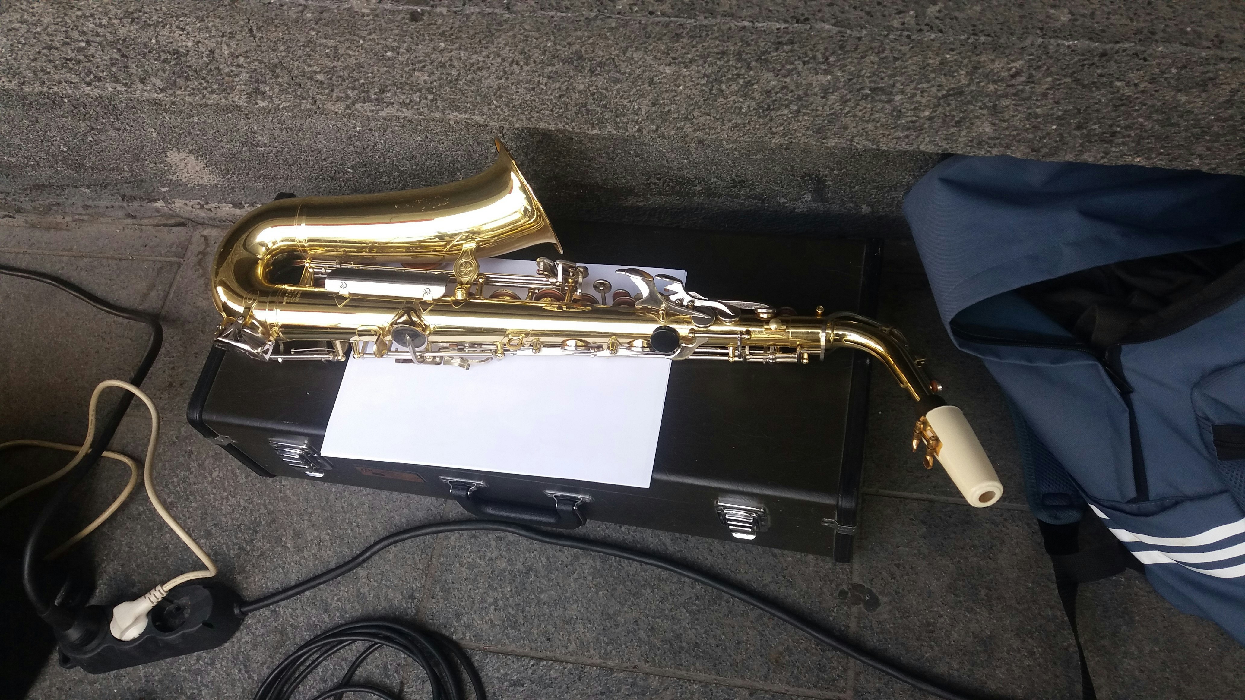 A gleaming saxophone rests on a black case, accompanied by a blank sheet of paper, suggesting a moment of musical anticipation.