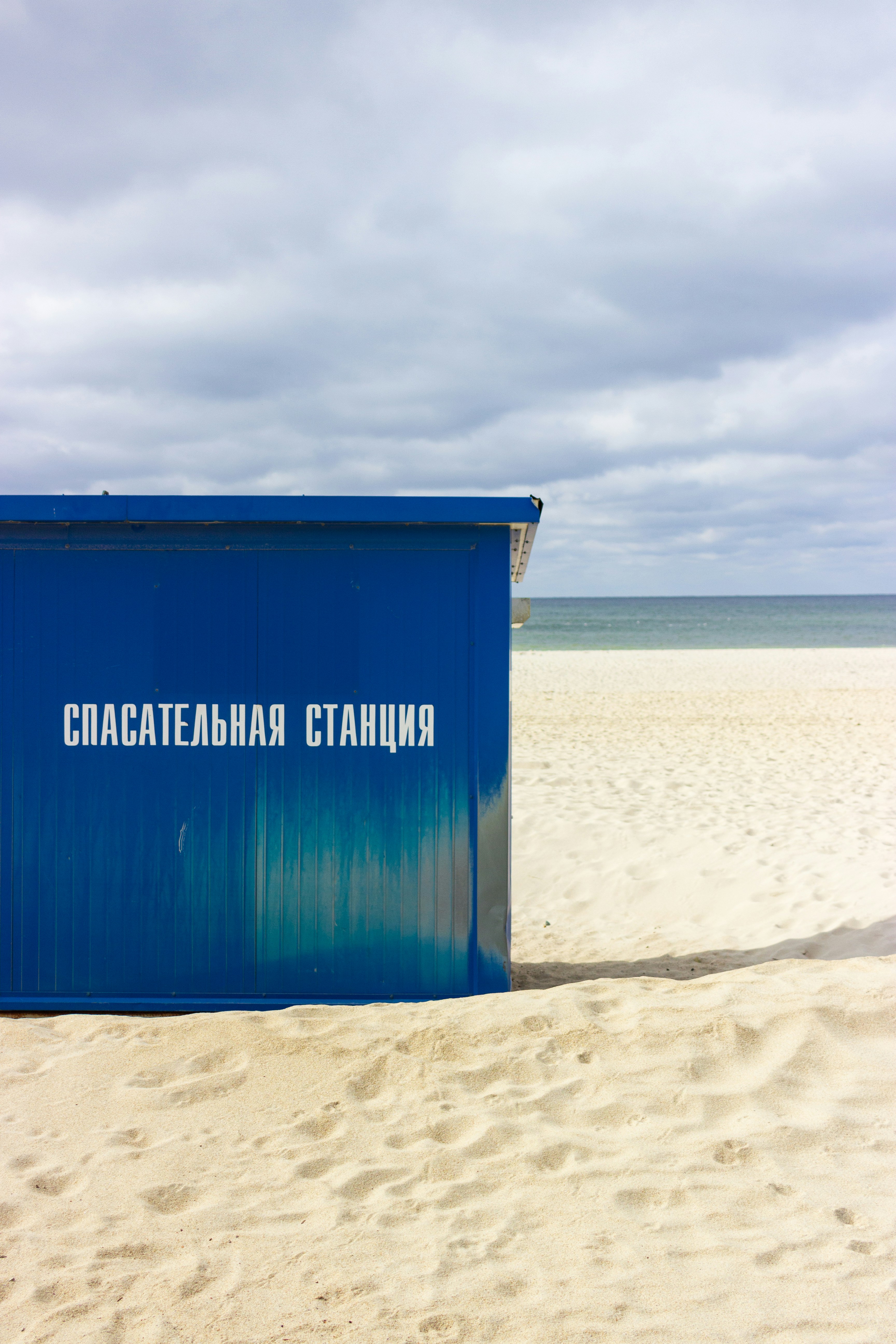 Bright blue lifeguard station stands on a sandy beach under a cloudy sky, emphasizing its role in beach safety.