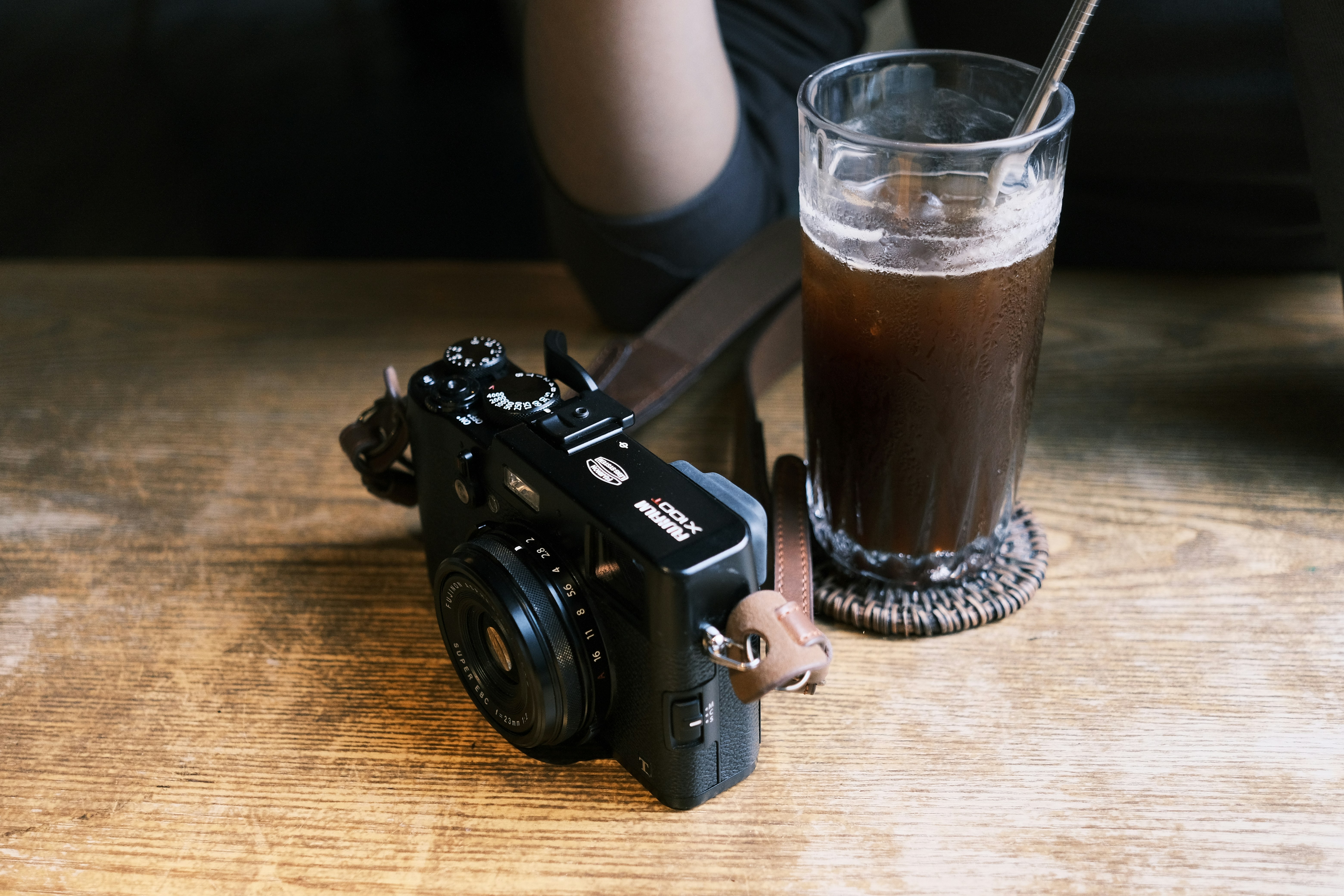 Café Gear Silence: A Fujifilm Camera Paused by Iced Coffee on Weathered Wood