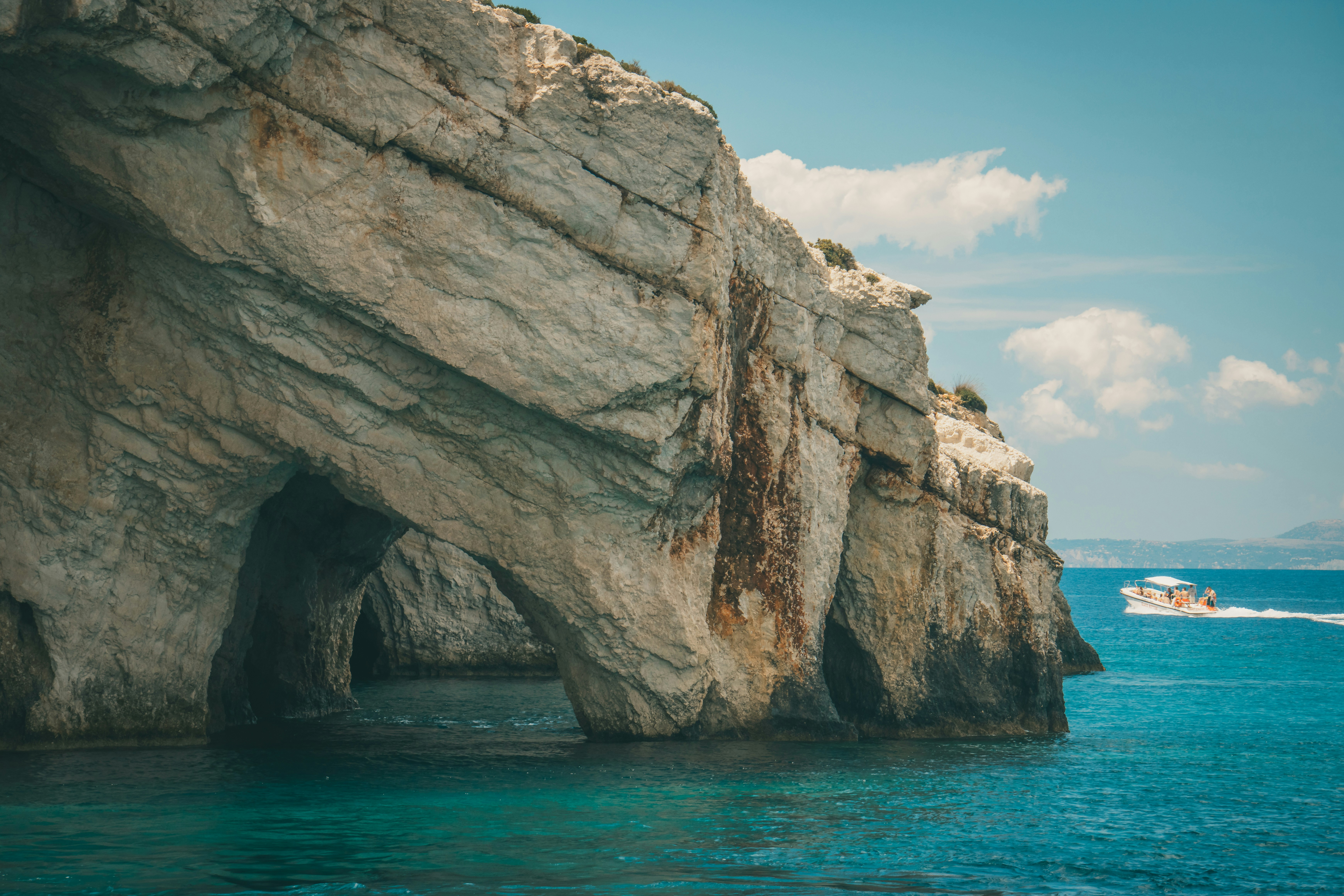 A boat is in the water near a large rock formation photo – Free Land ...