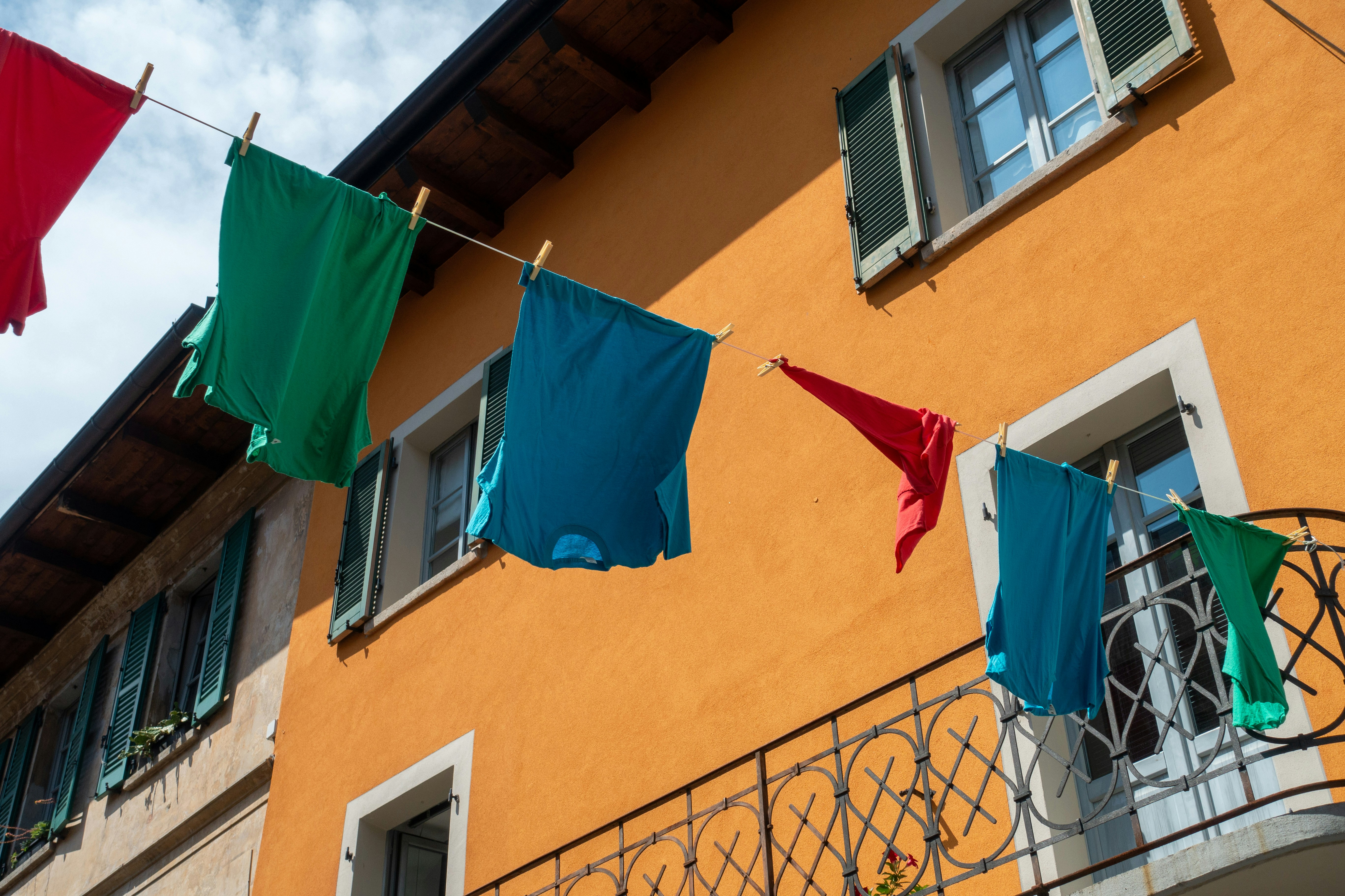 Vibrant clothes hang on a clothesline against a bright orange wall, showcasing a mix of colors and textures. The scene captures the essence of everyday life.