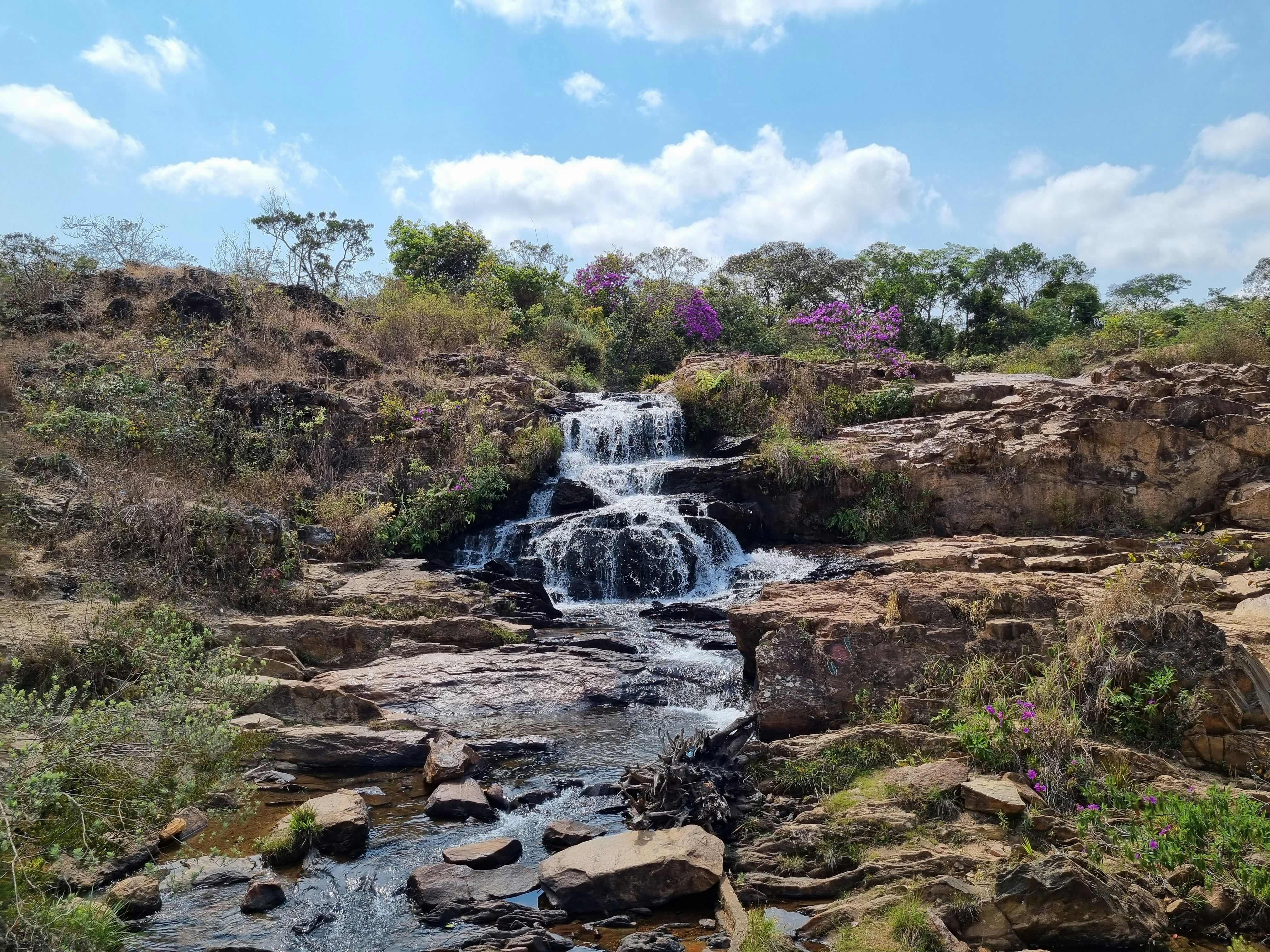 Small waterfall cascading over rocky terrain under a bright blue sky.