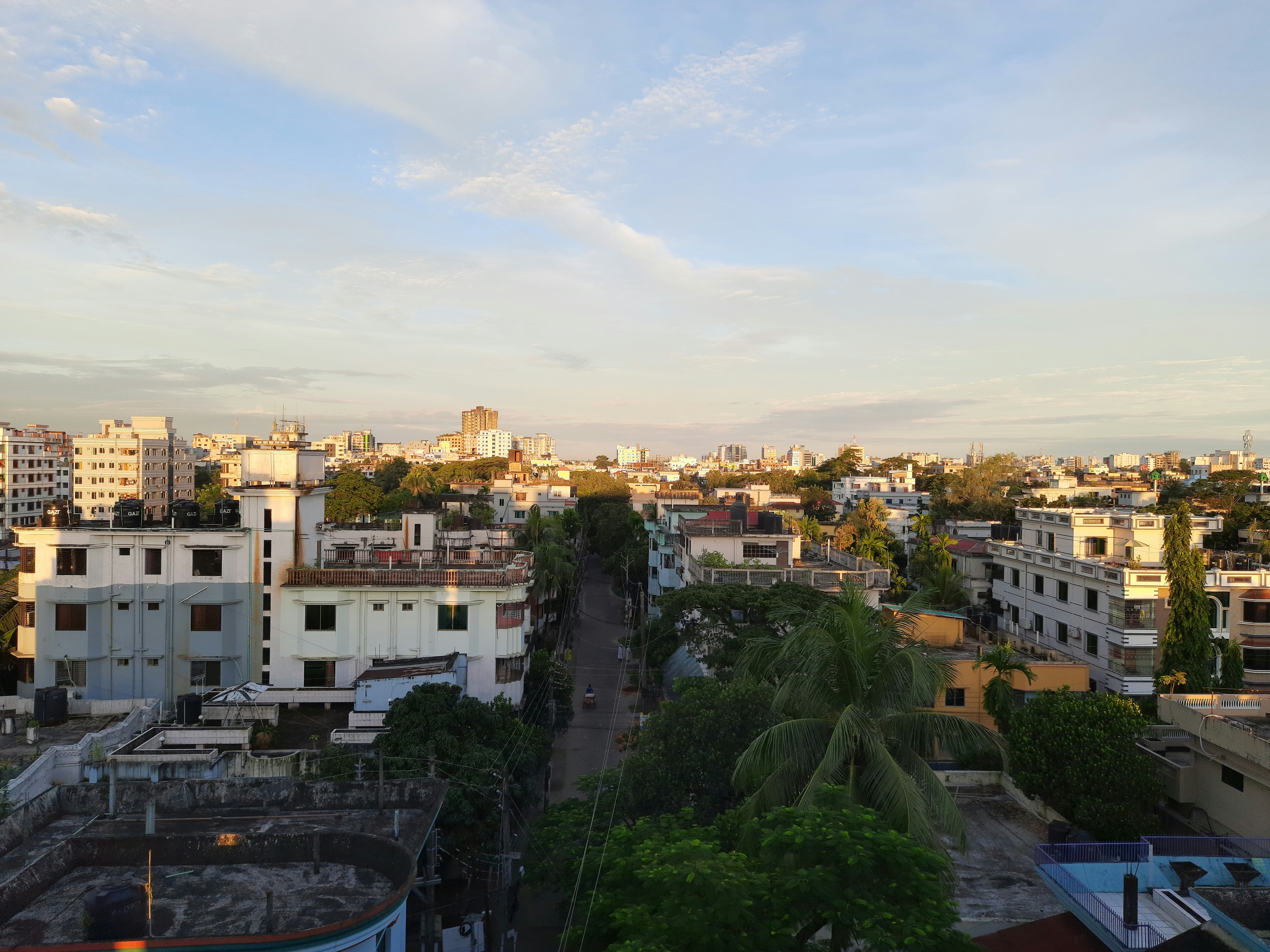 A panoramic view of a cityscape bathed in warm evening light, showcasing a blend of modern and traditional architecture along a quiet street.