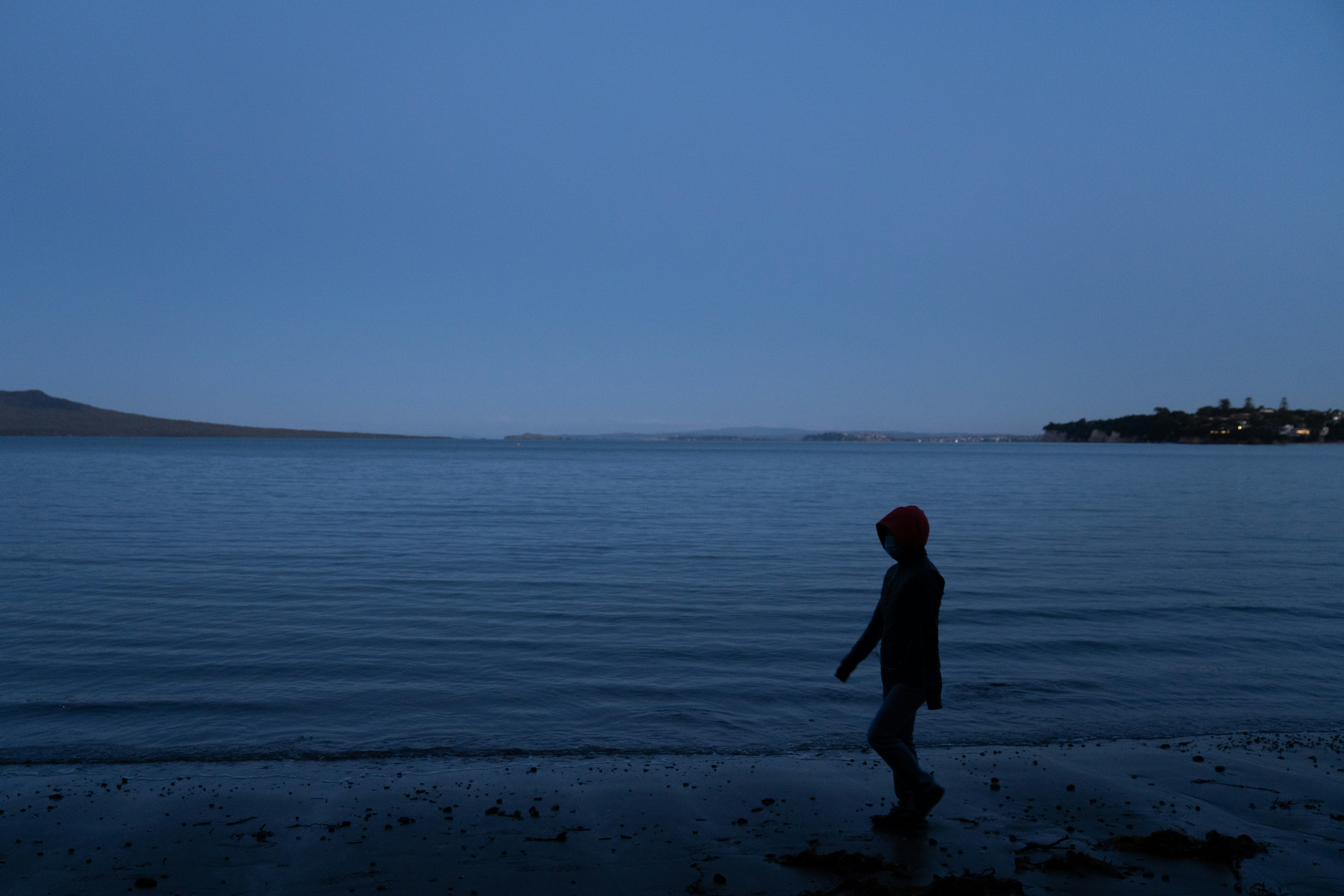 Blue Hour Silhouette: A lone walker crosses a calm shoreline under a cobalt sky.