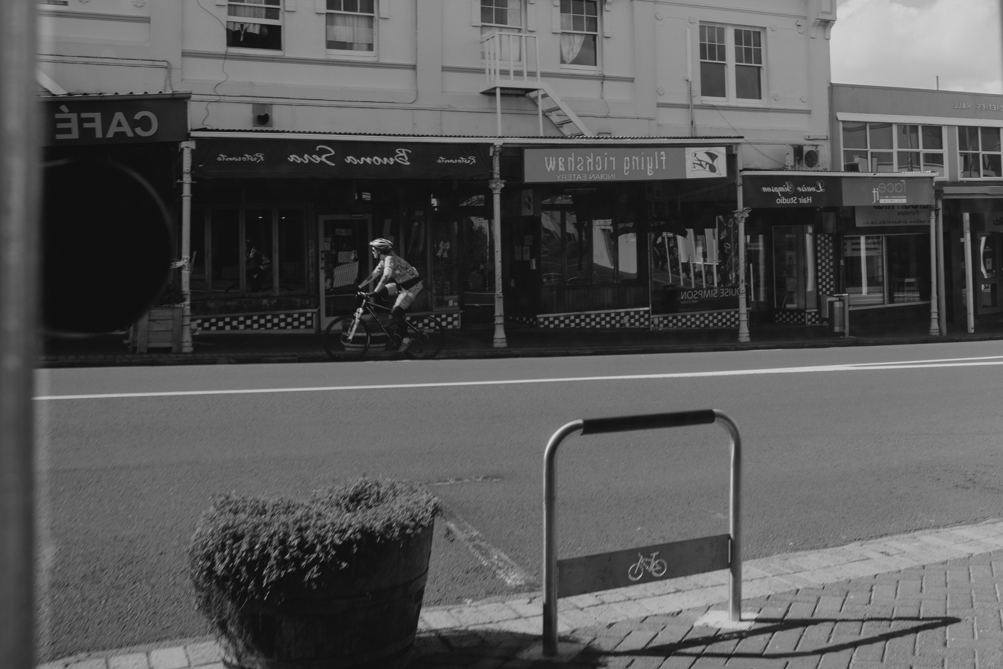 Grey Street Rhythm: Cyclist Crossing a Shopfront Corridor
