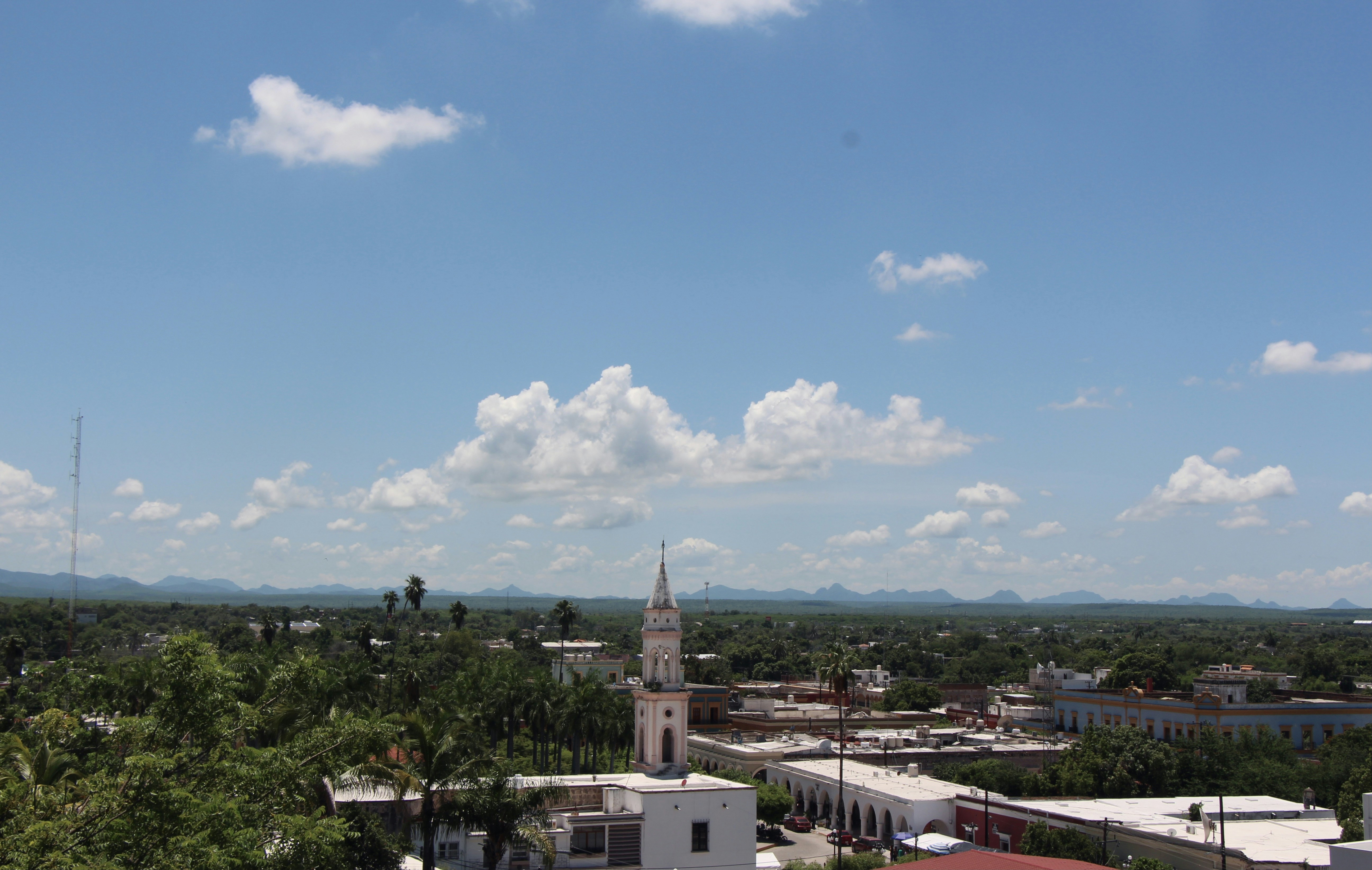 A picturesque view of a town featuring a historic church steeple surrounded by lush greenery and distant mountains under a vibrant sky.