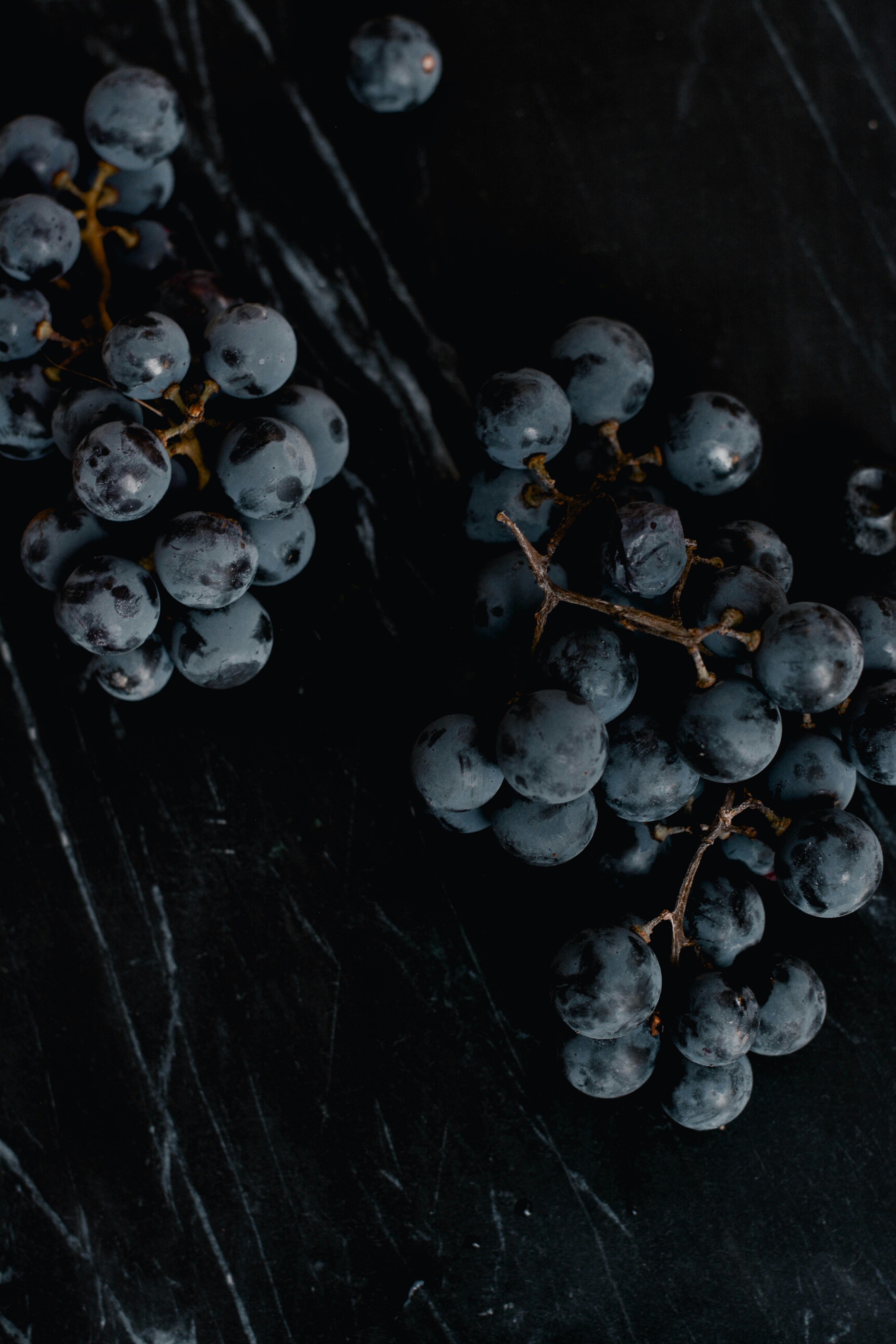 Dark purple grapes arranged elegantly on a textured black surface, highlighting their natural sheen and rich color.