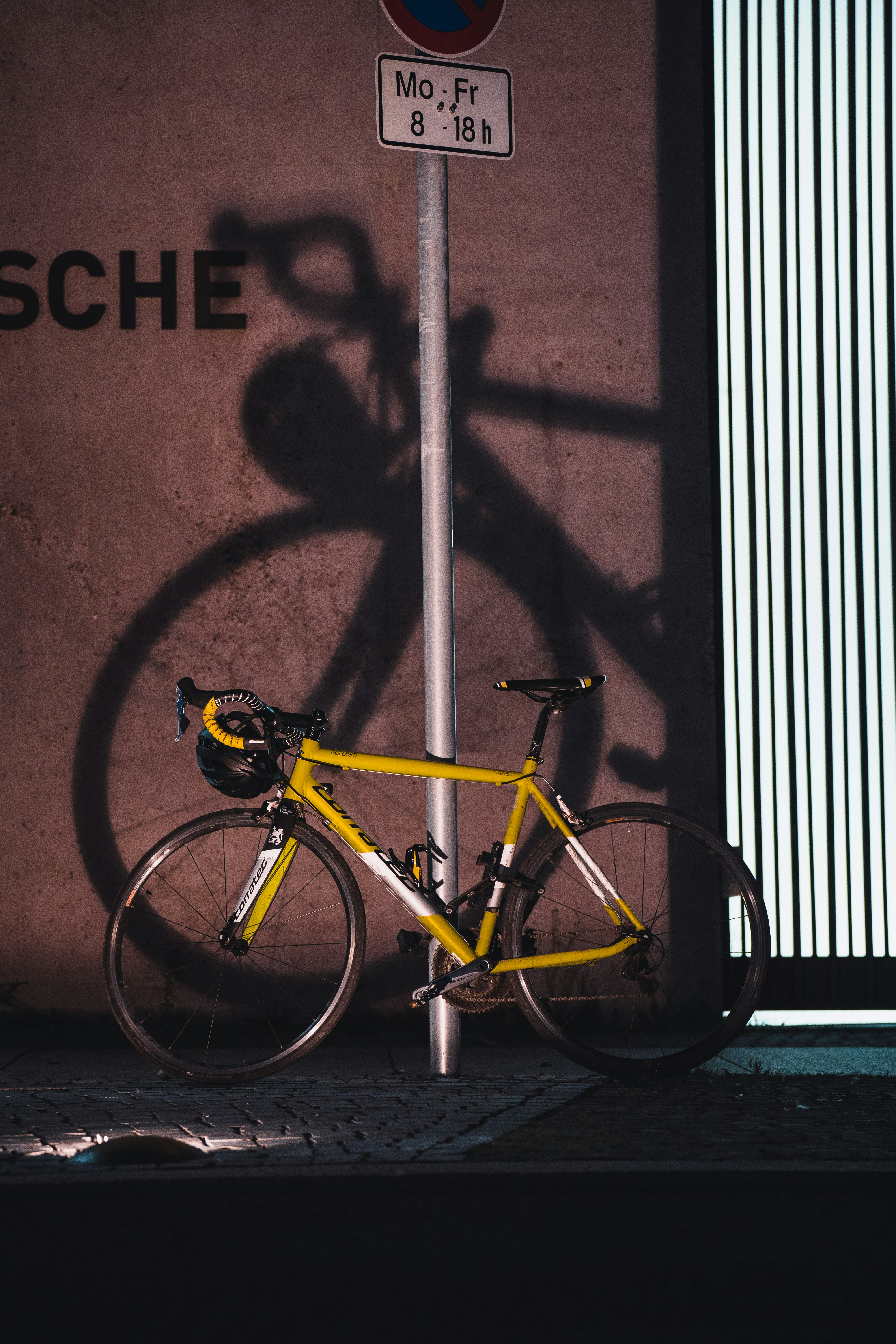 A bike standing next to a ground light, throwing big shadows at a wall. 
