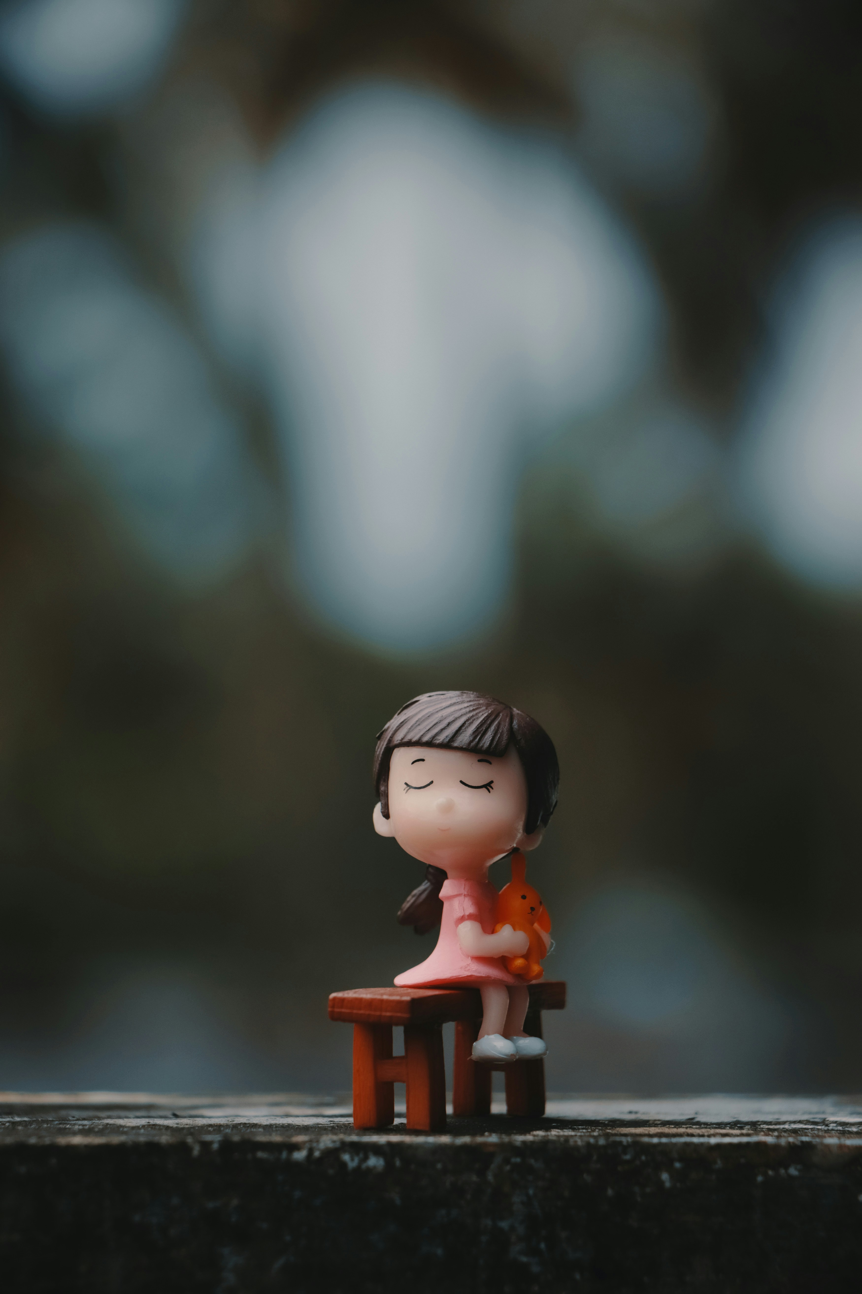 A charming figurine of a girl sitting on a small wooden bench, holding a cat, with a softly blurred background that enhances the sense of tranquility.