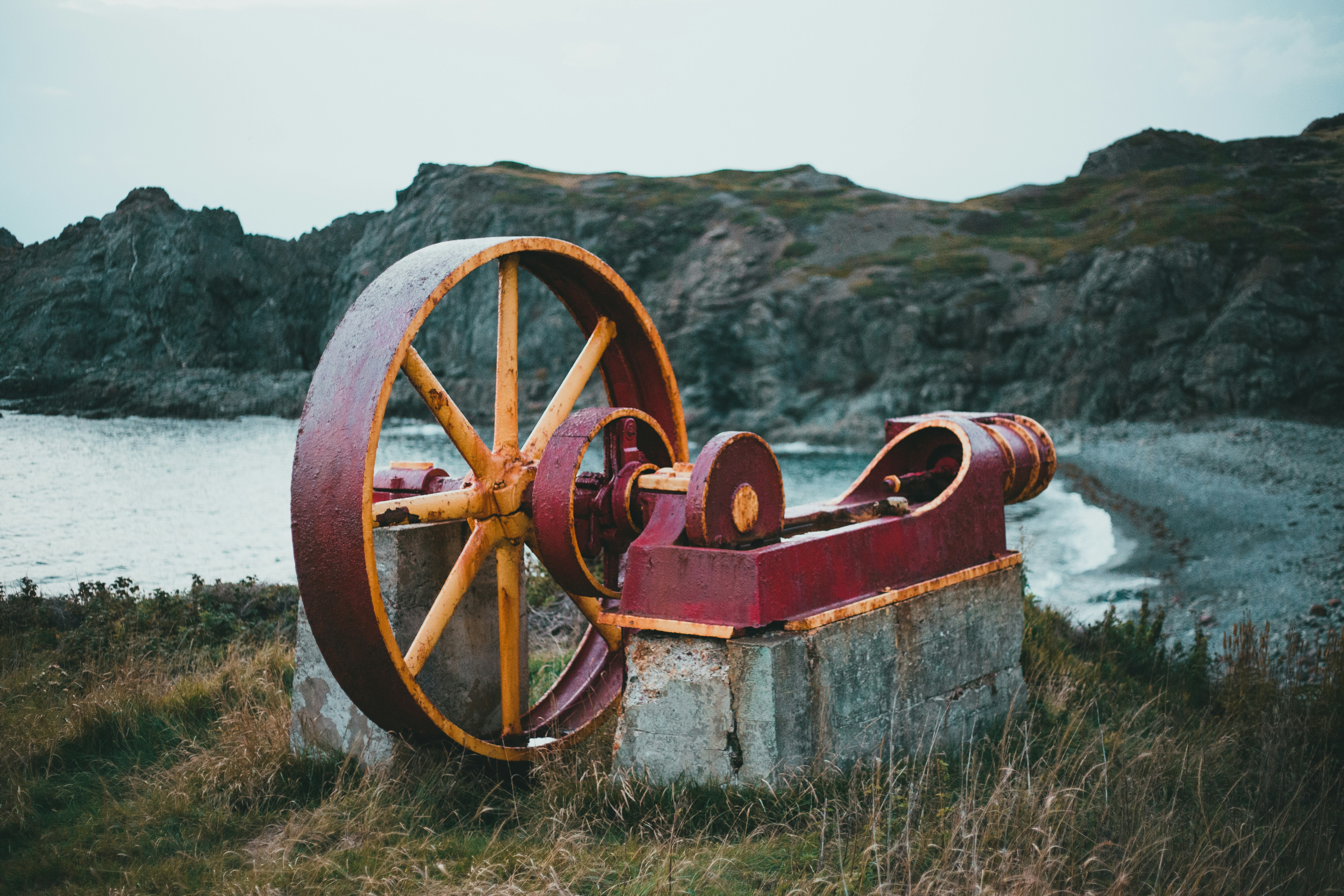An old rusted water pump sitting in a field next to a body of water ...