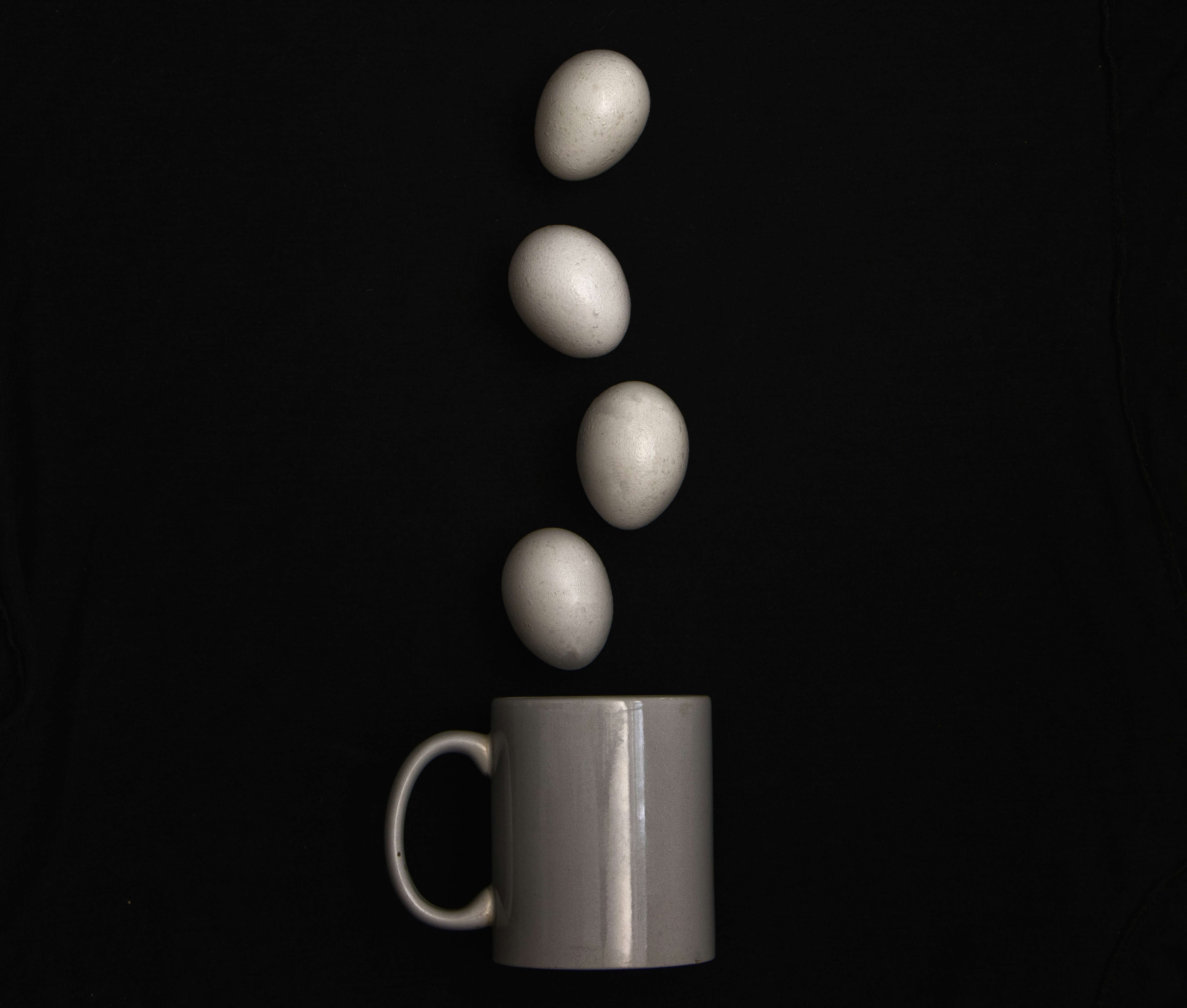 Five White Eggs Align in a Vertical Stack Above a White Mug