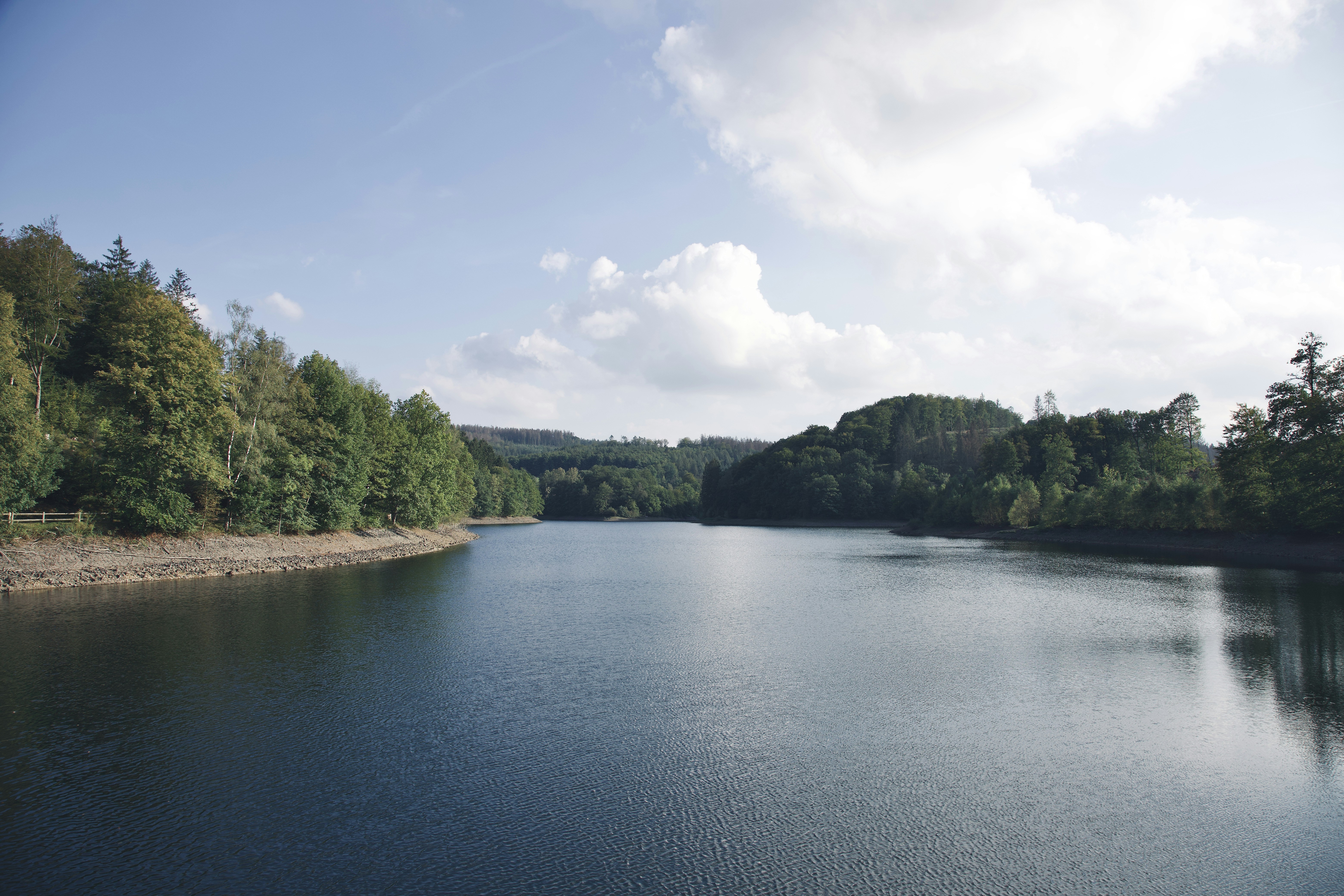 Tranquil lake reflecting lush greenery and a clear sky, framed by gentle hills. The scene embodies the peacefulness of nature.