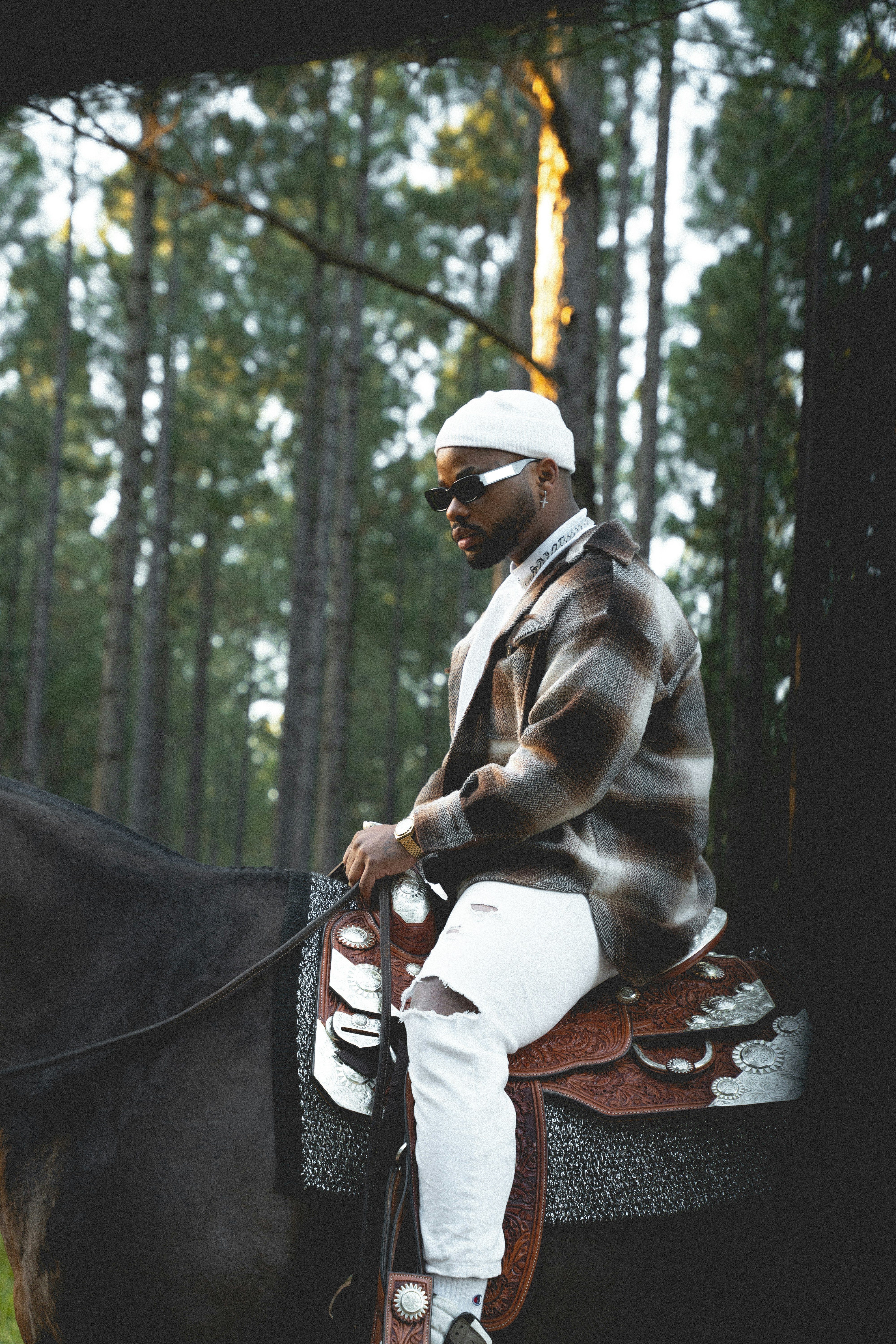 A rider in stylish attire sits confidently on a horse, surrounded by tall trees in a tranquil setting.
