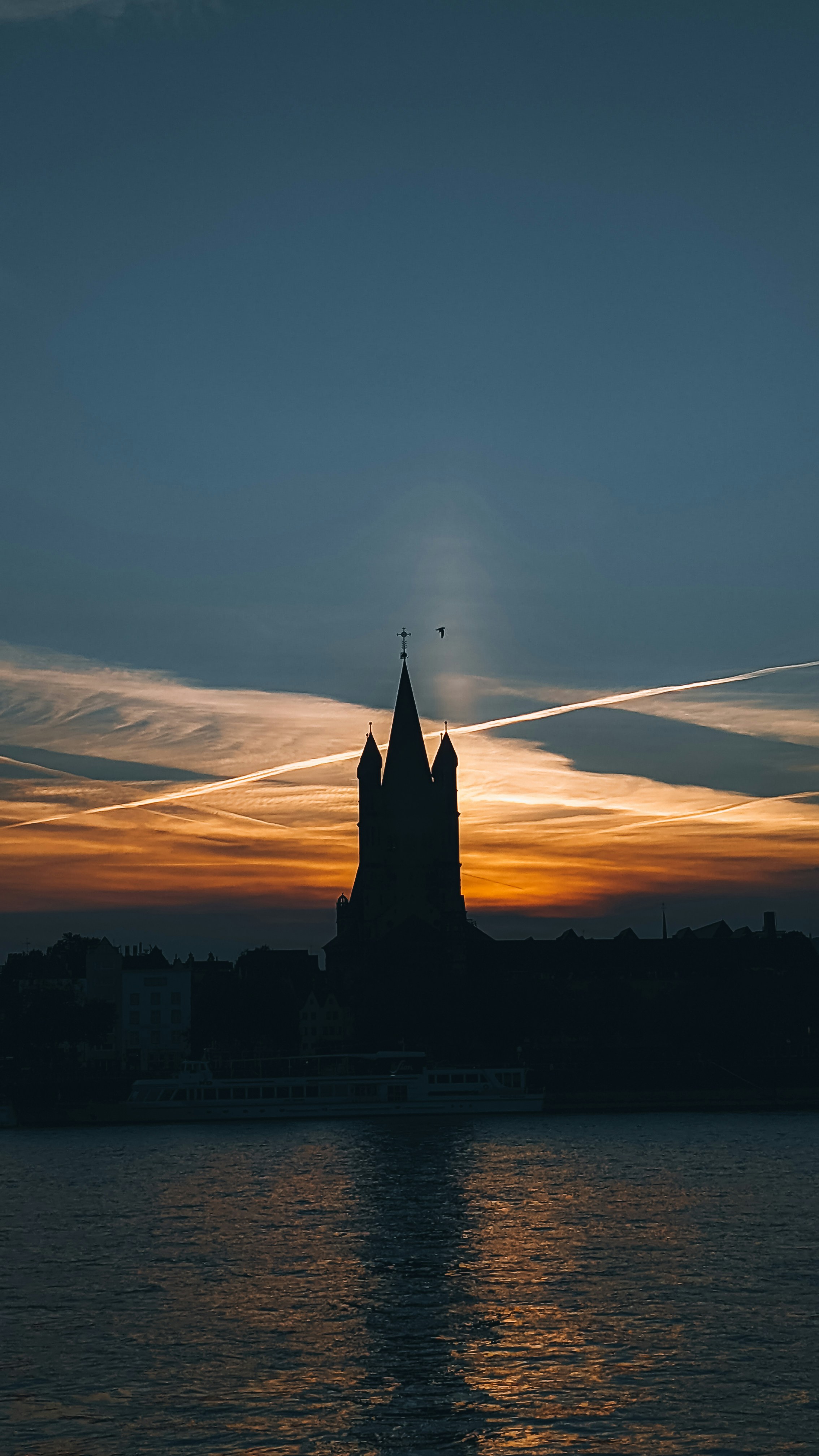 Twin Spires at Dusk: Waterfront Silhouette Beneath a Sky of Contrails