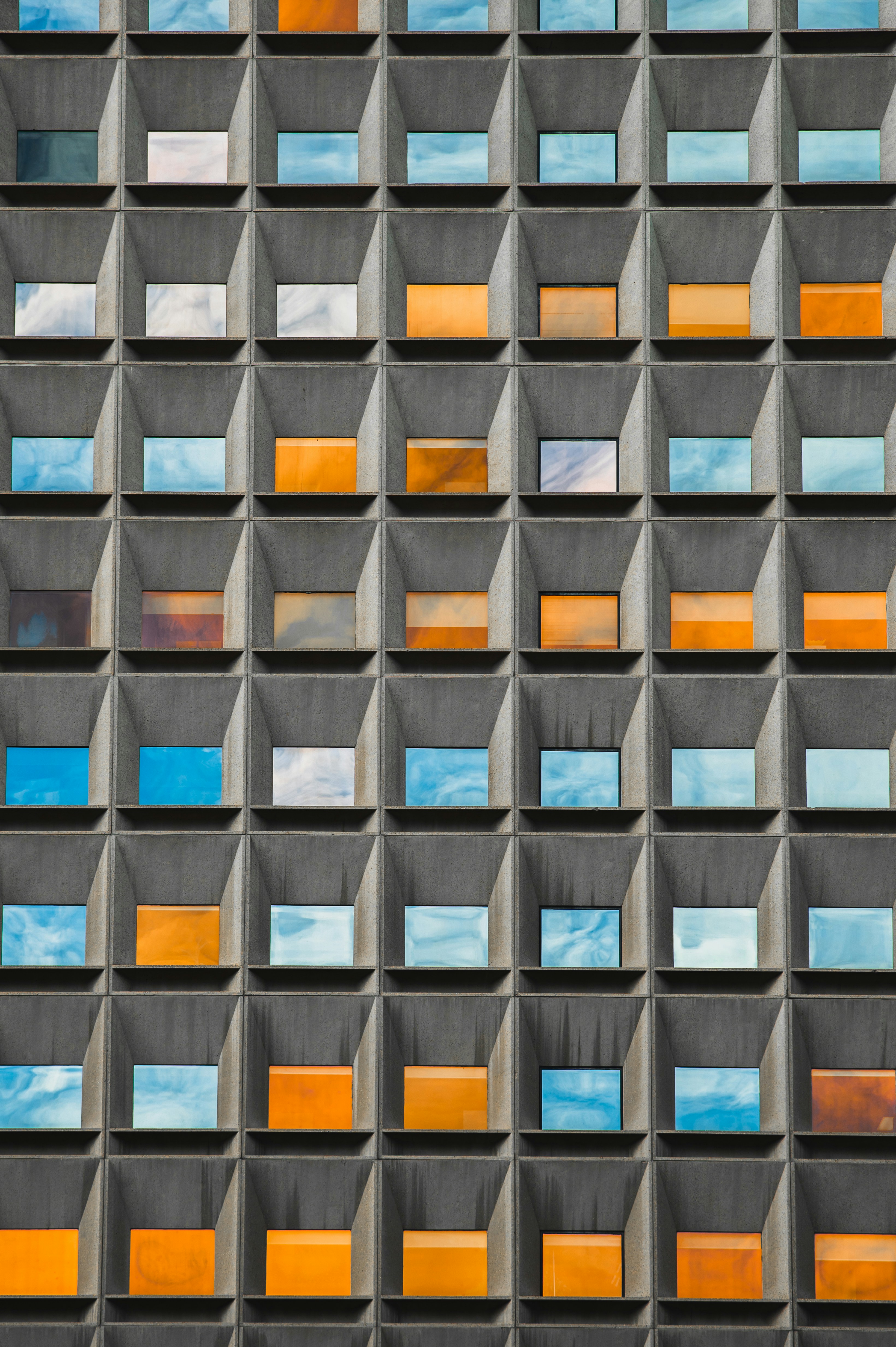 Geometric facade of a modern building featuring a grid of windows reflecting the sky and cityscape.