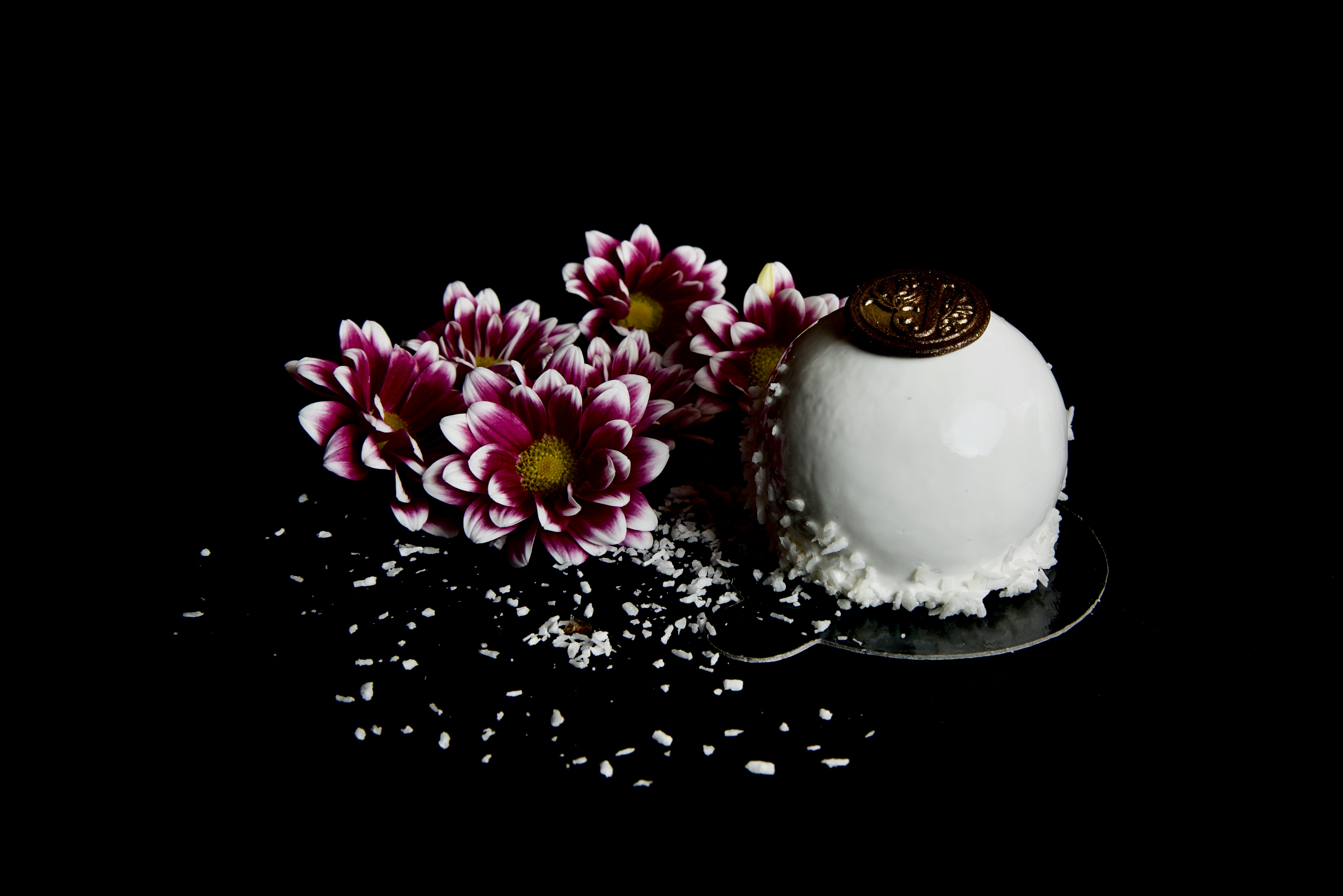 Glossy White Dessert Dome Amid Magenta Chrysanthemums on a Black Stage