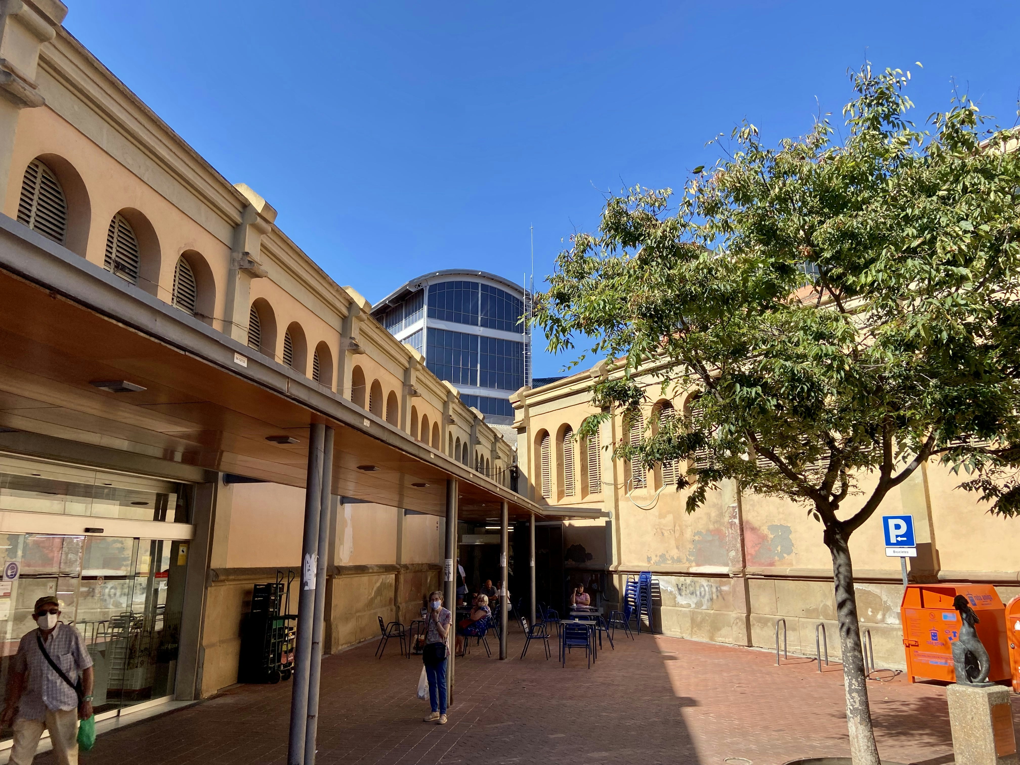 Historic Catalonian market entrance with arched windows and a vibrant courtyard under a clear blue sky.