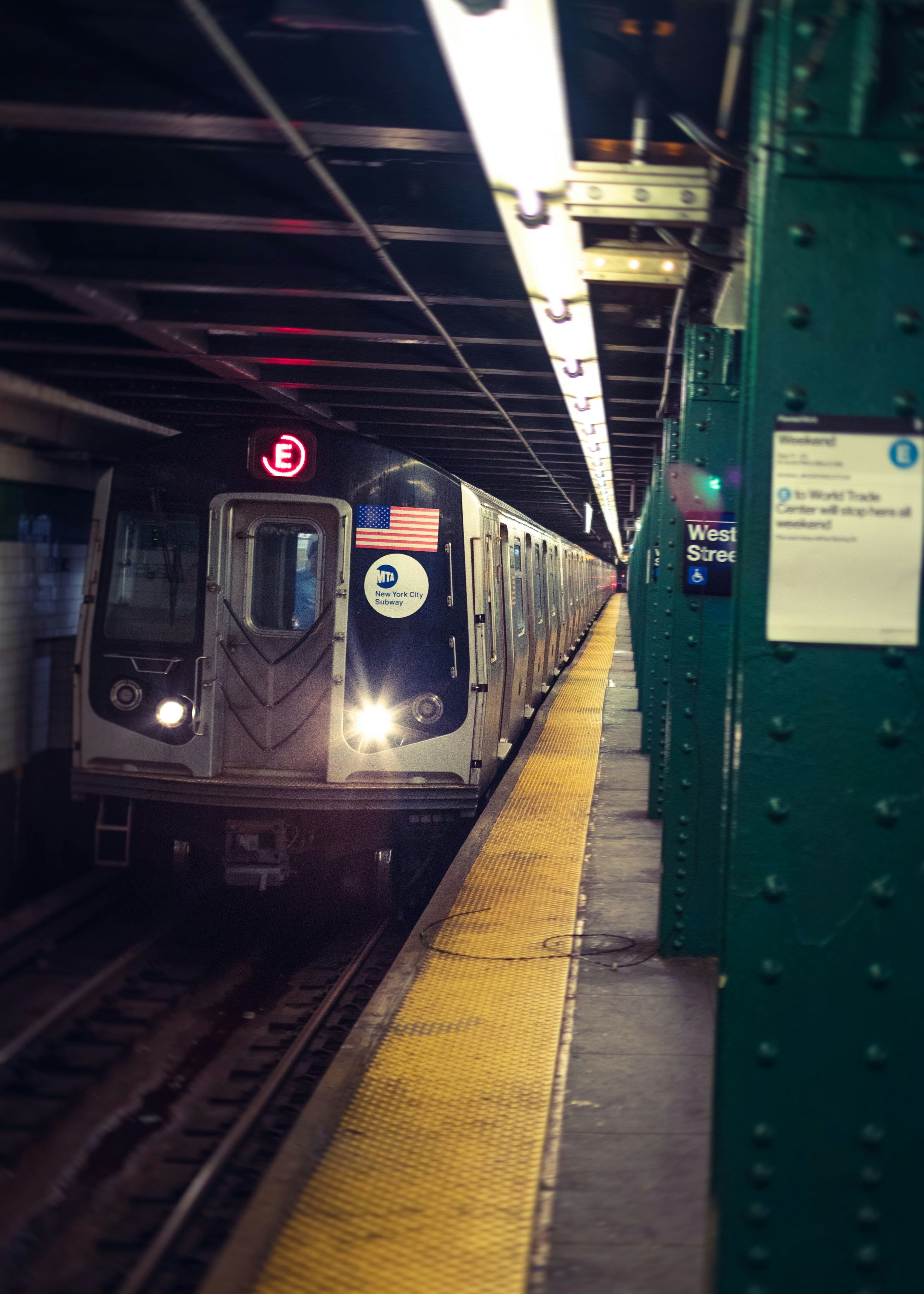 Subway train approaching platform in a bustling underground station, illuminated by overhead lights. The scene captures the essence of urban commuting.