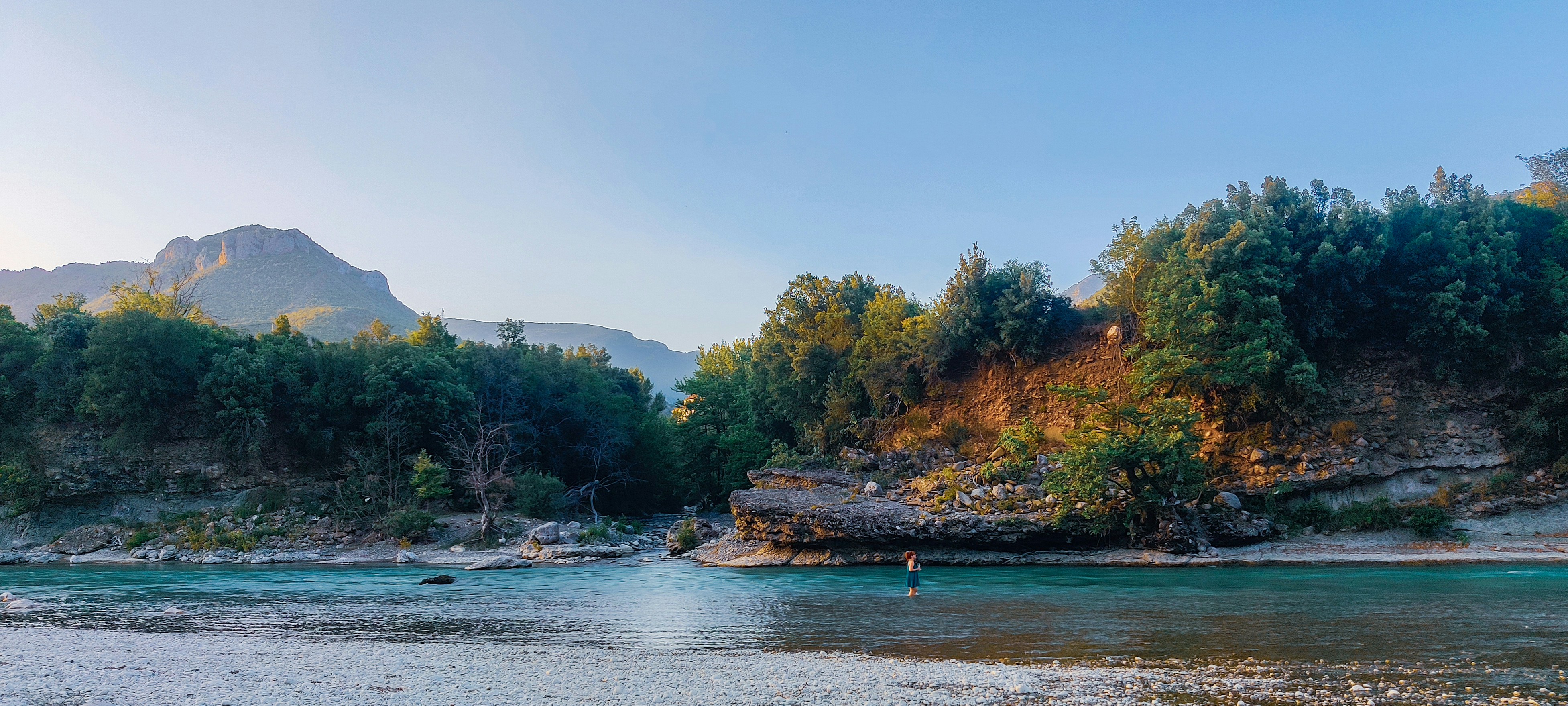 Lone Swimmer at a Sunlit River Bend with Forested Cliffs