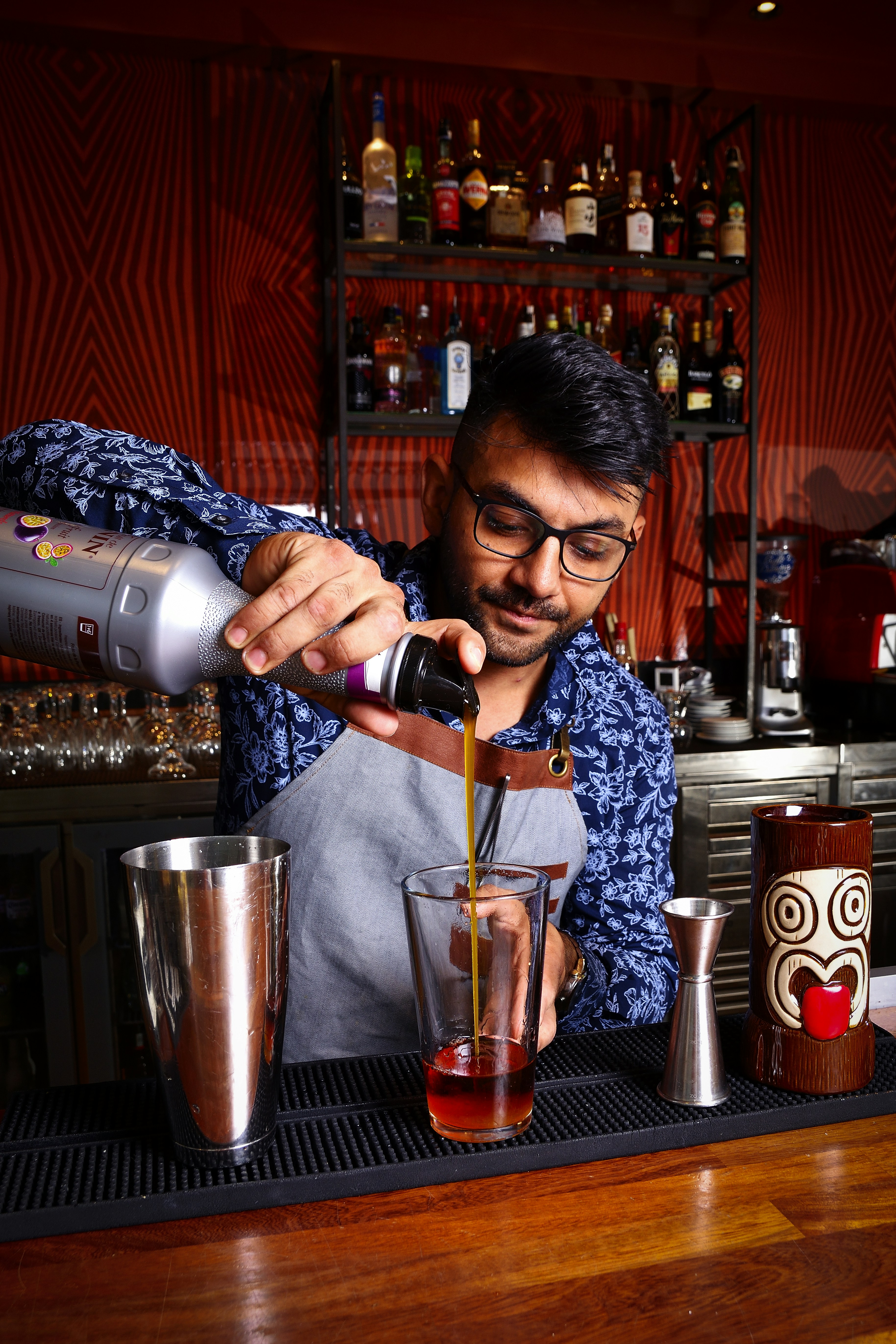 Bartender skillfully pouring a cocktail into a glass, showcasing a vibrant bar setup with various bottles in the background.