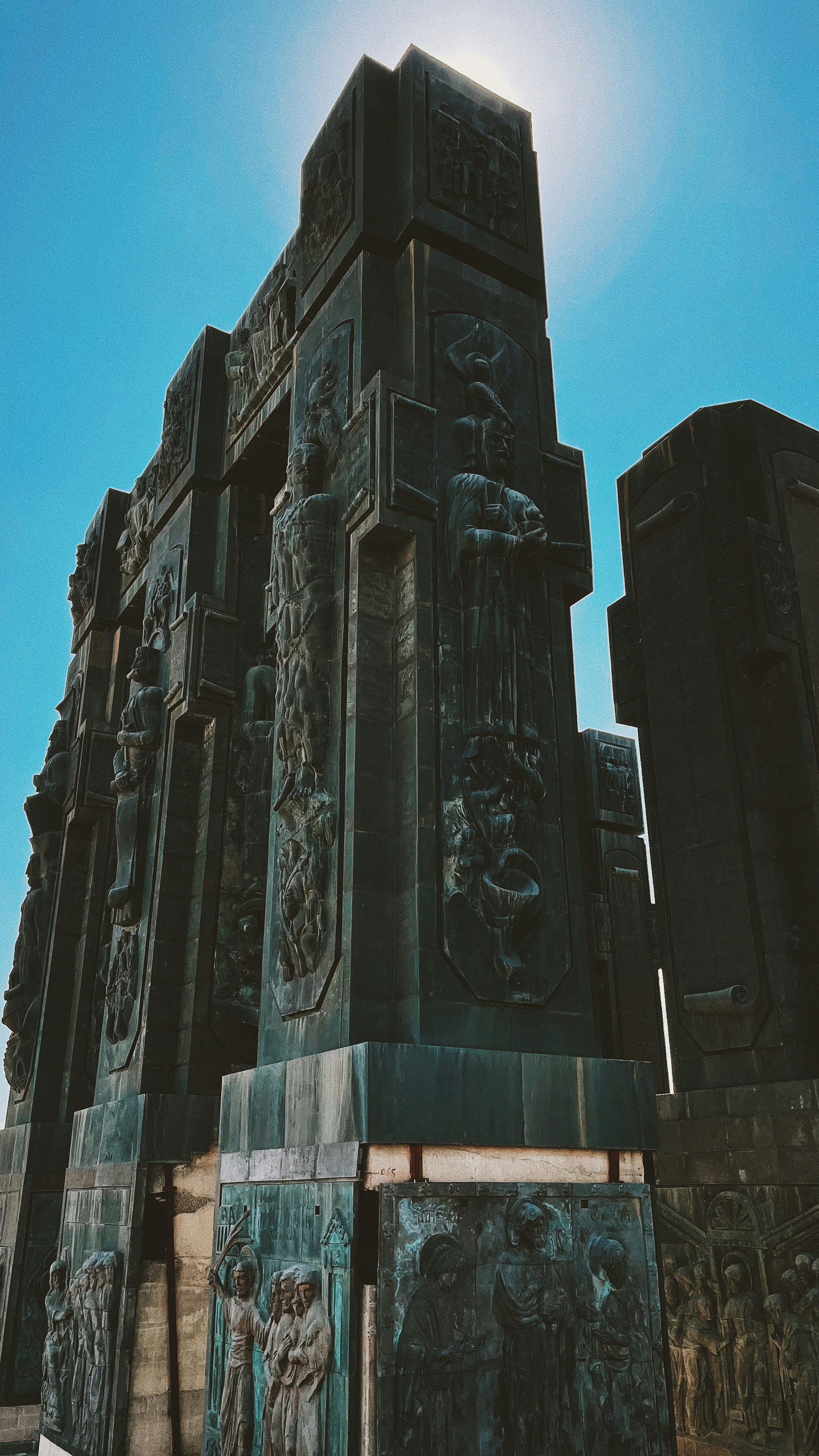 Intricate stone carvings on towering pillars, illuminated by sunlight against a clear blue sky.