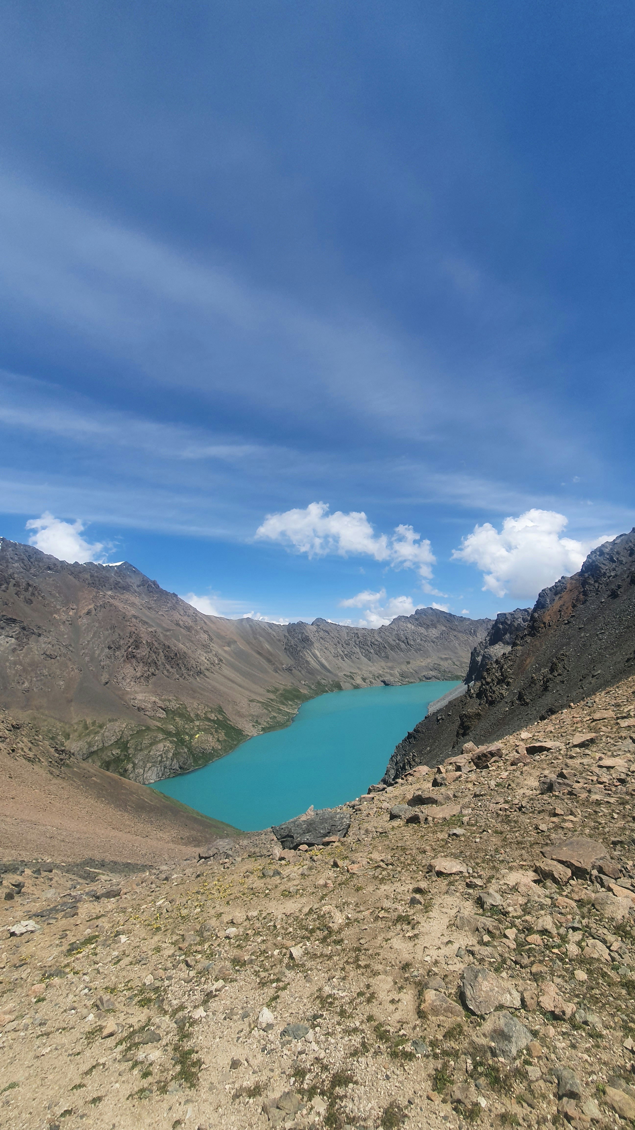 Vibrant turquoise lake nestled between rugged mountains under a bright blue sky with scattered clouds.