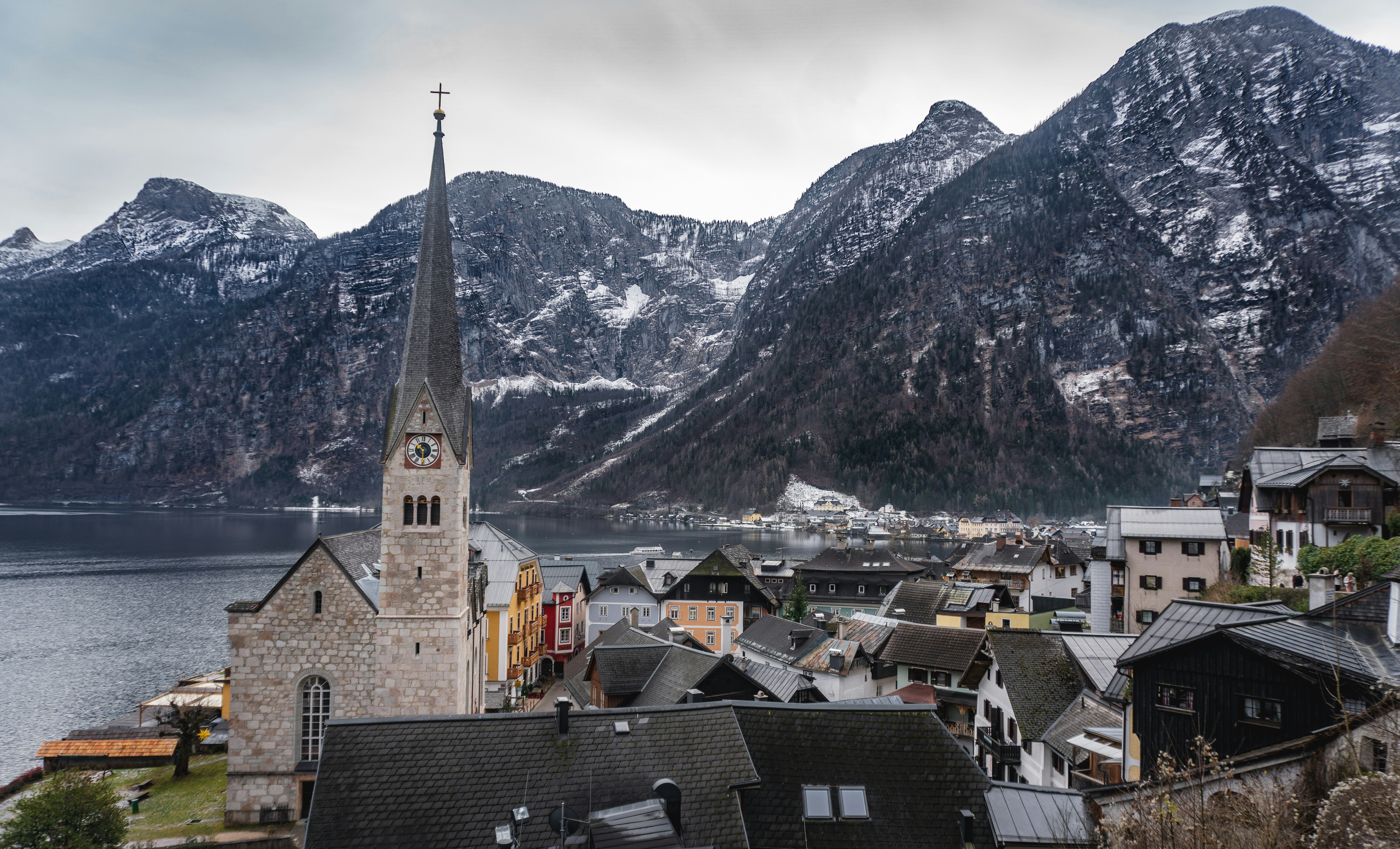 Historic church tower rises above quaint village, nestled between dramatic snow-capped mountains and serene waters.