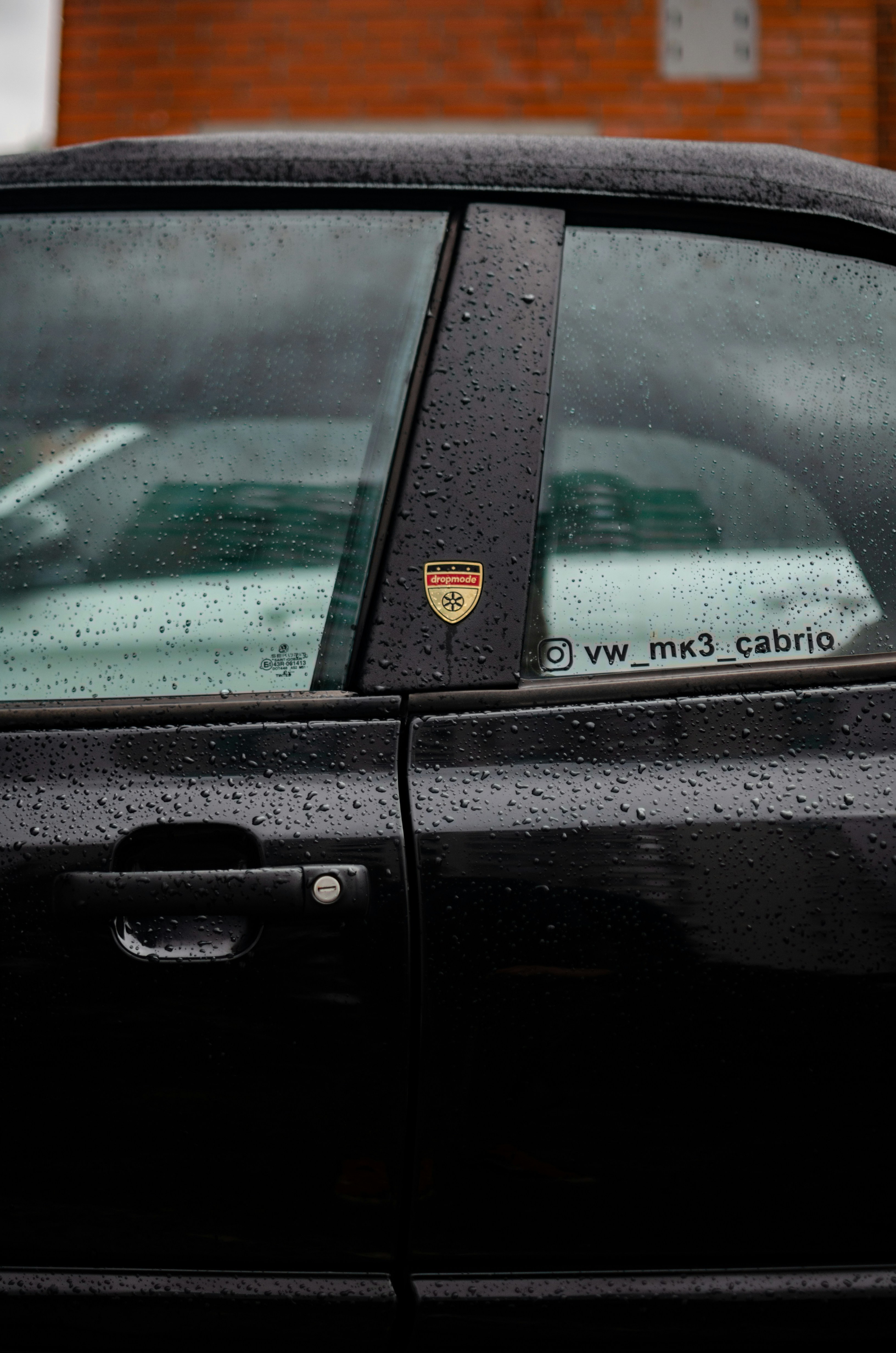 Rain-speckled Porsche crest on a midnight-black door
