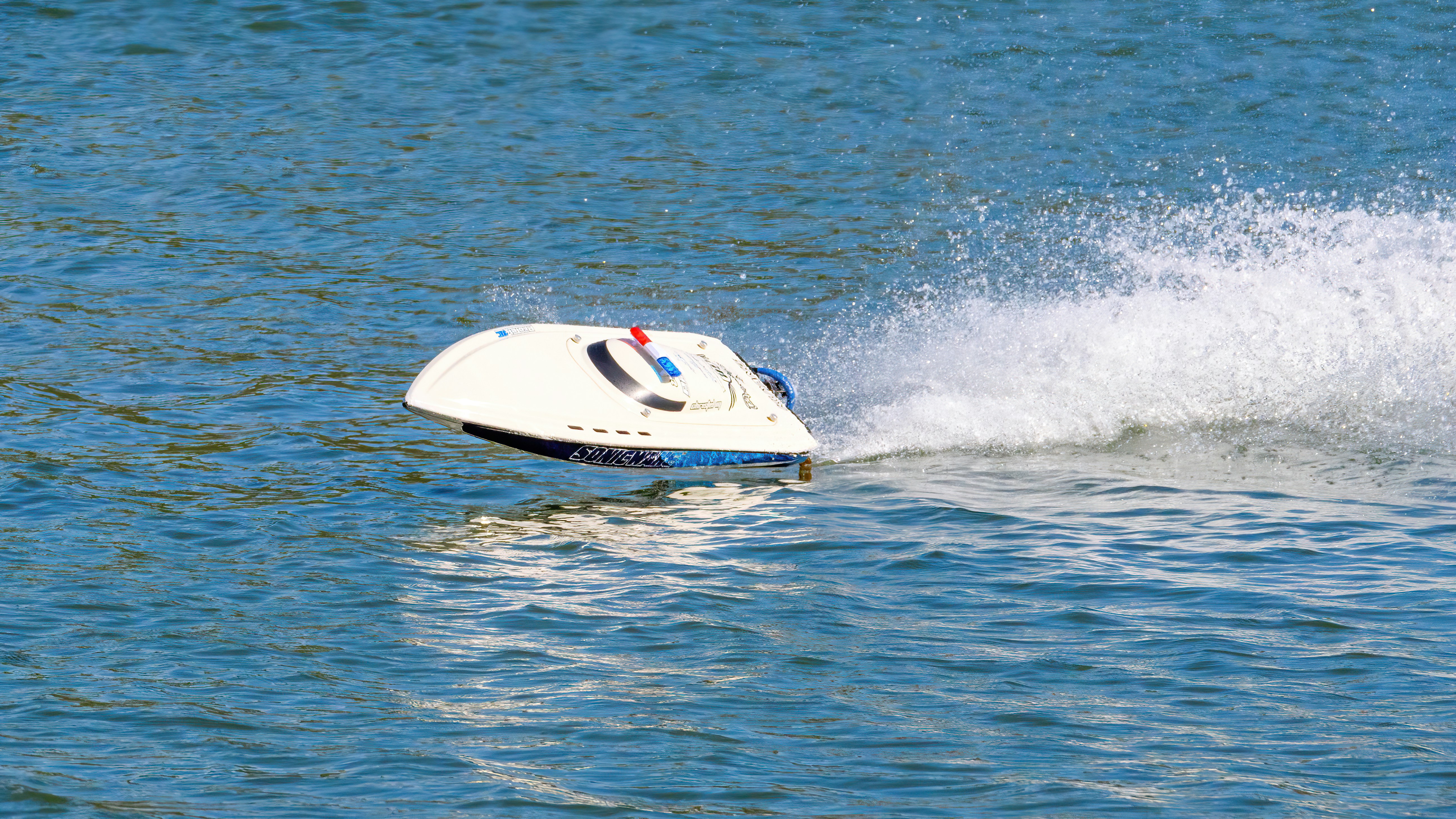 White speedboat skims across blue lake, leaving a spray of water