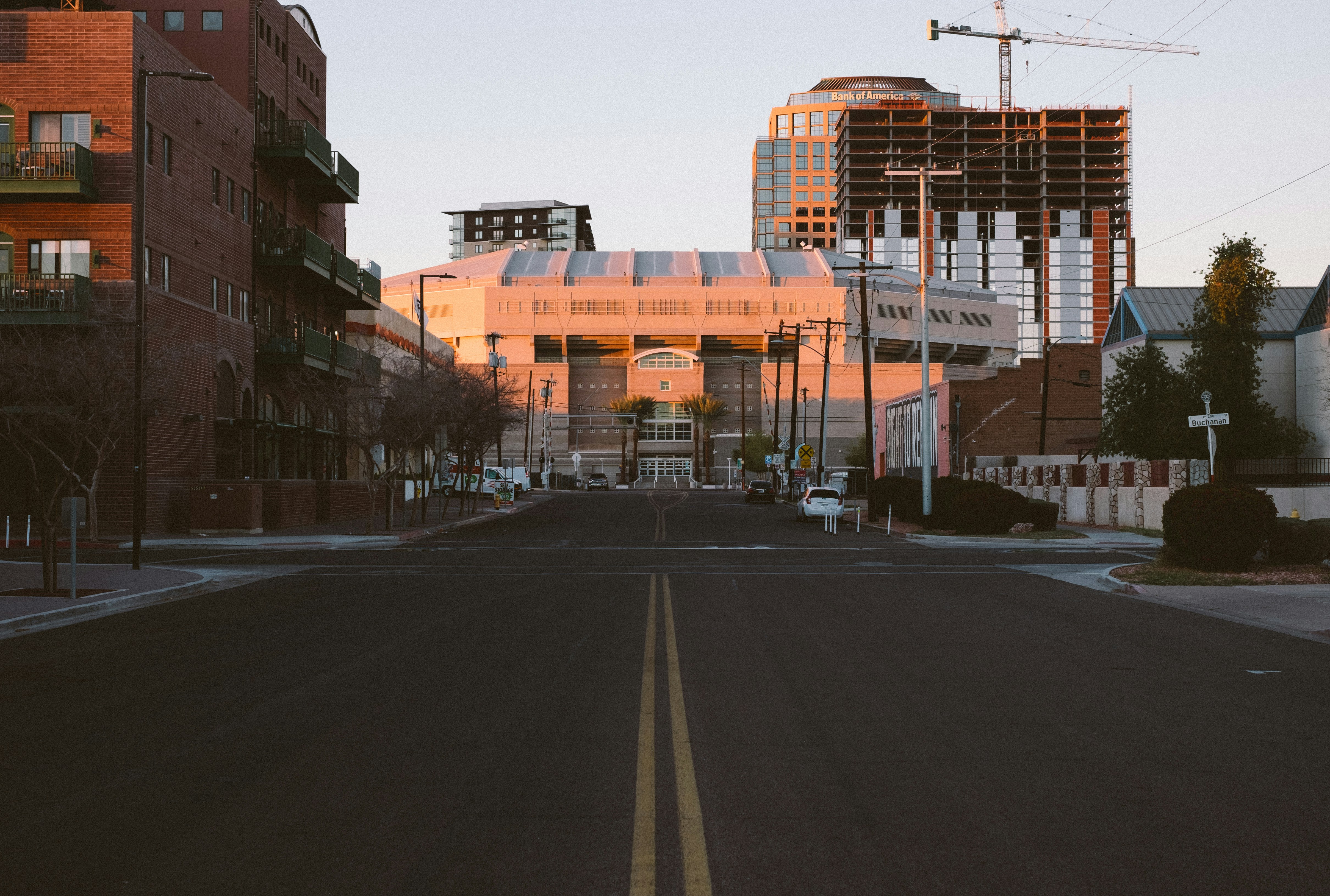 City street at dawn with a focus on modern architecture, showcasing a blend of old and new structures. The warm light highlights the emerging skyline.