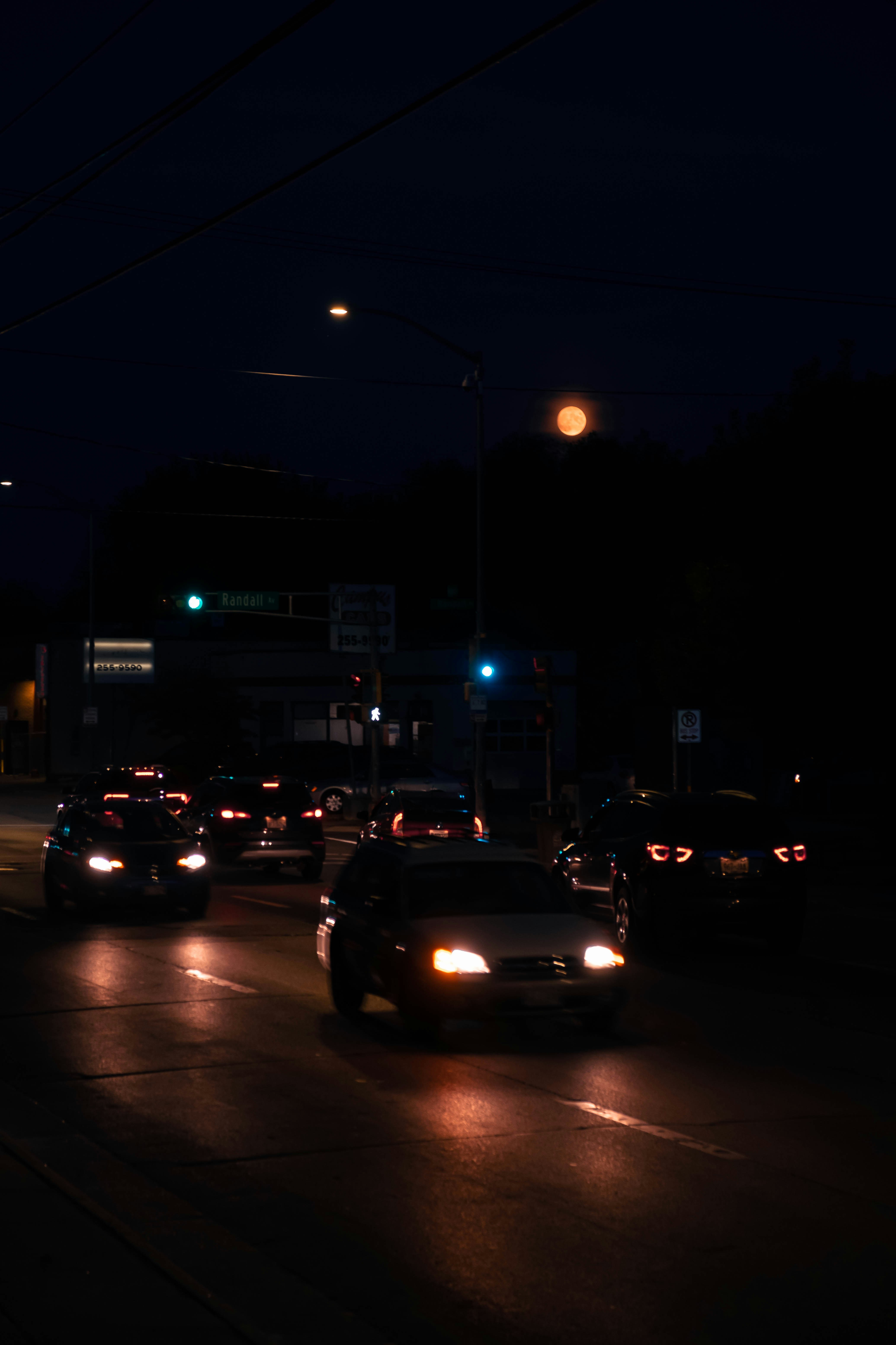 Cars navigating a city intersection under a bright moon, with traffic lights illuminating the scene.
