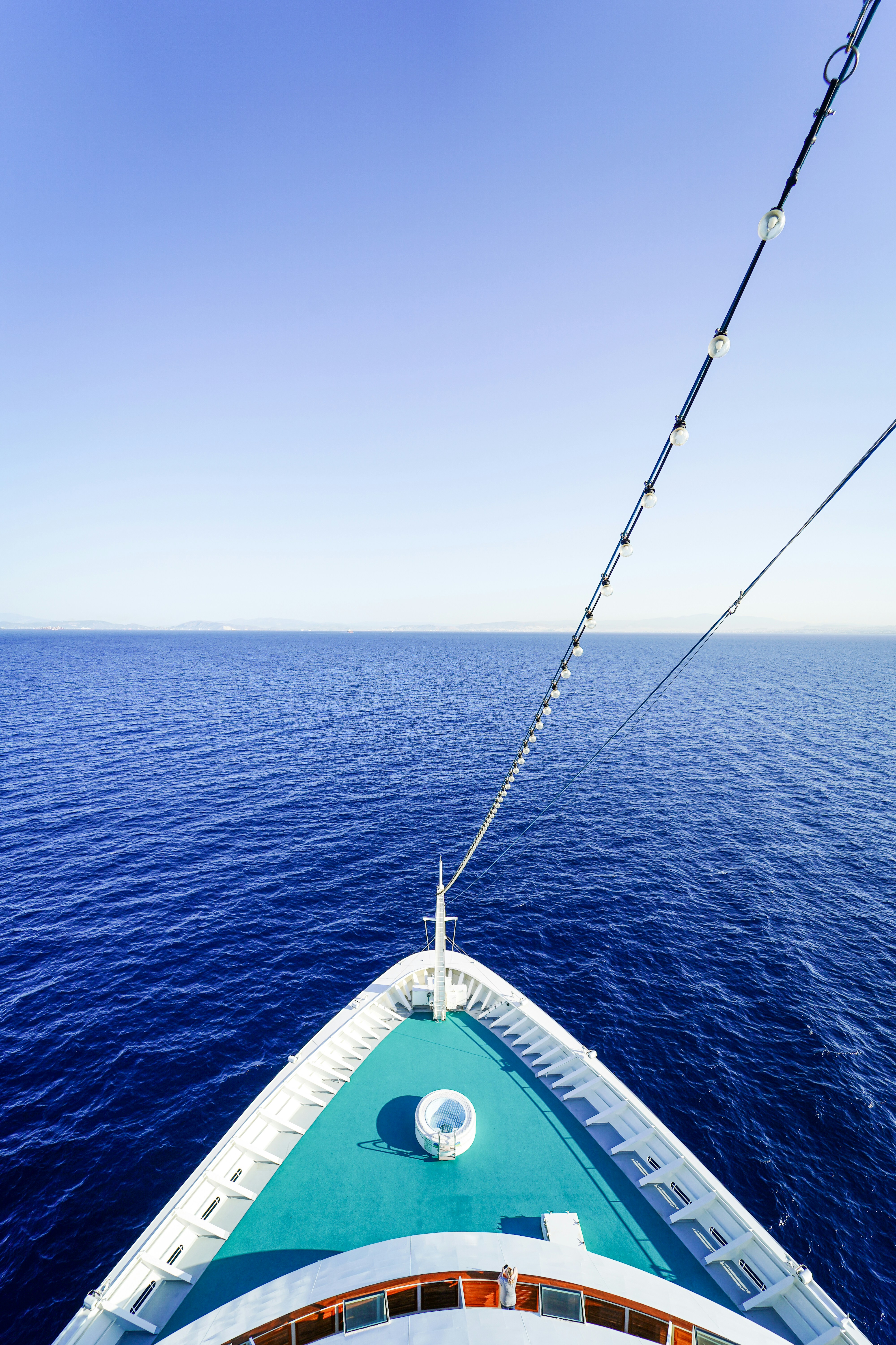 Bow of a cruise ship cutting through the calm, deep blue sea under a clear sky.