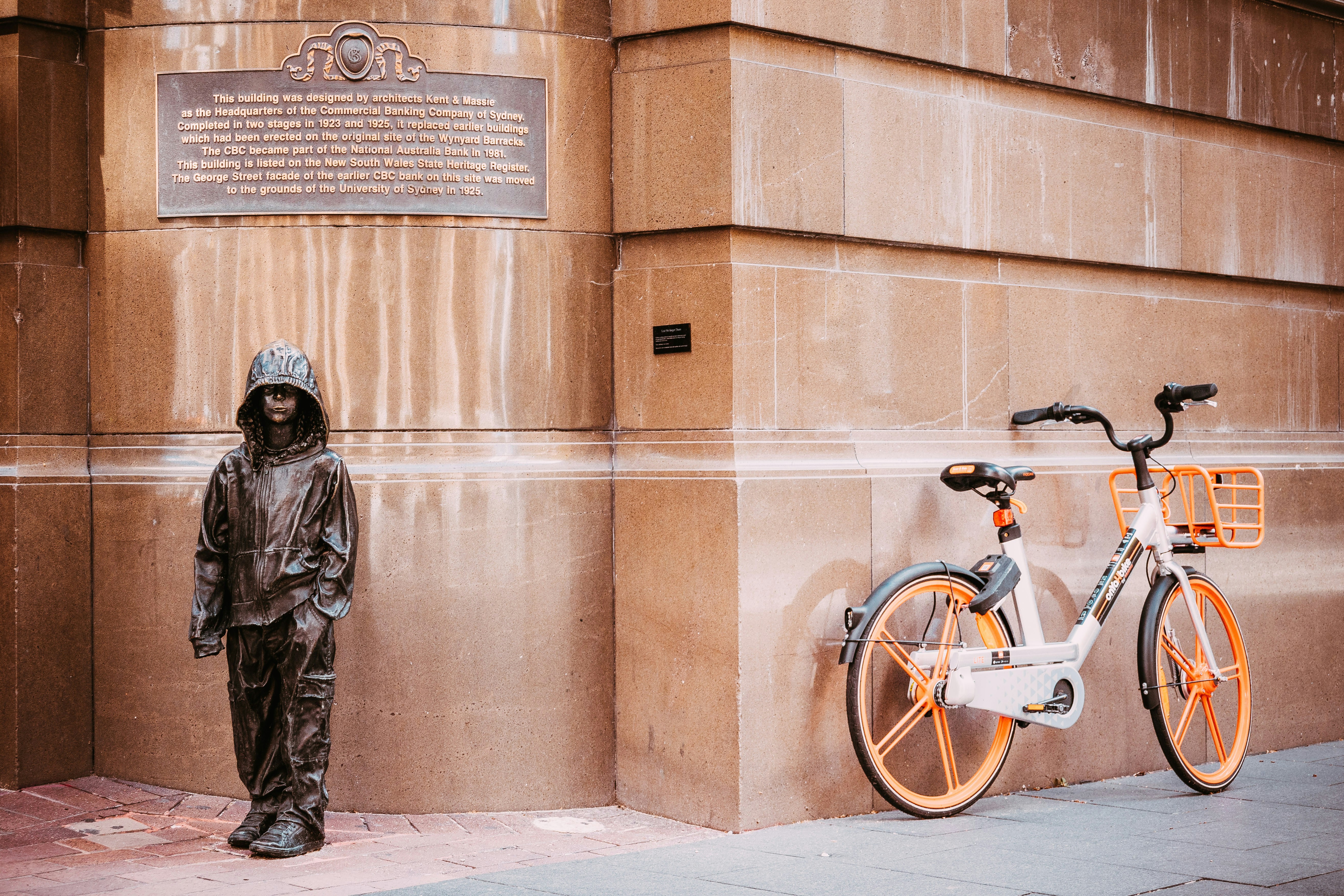 Bronze Sentinel on a City Wall, Paired with an Orange-Tinted Bike