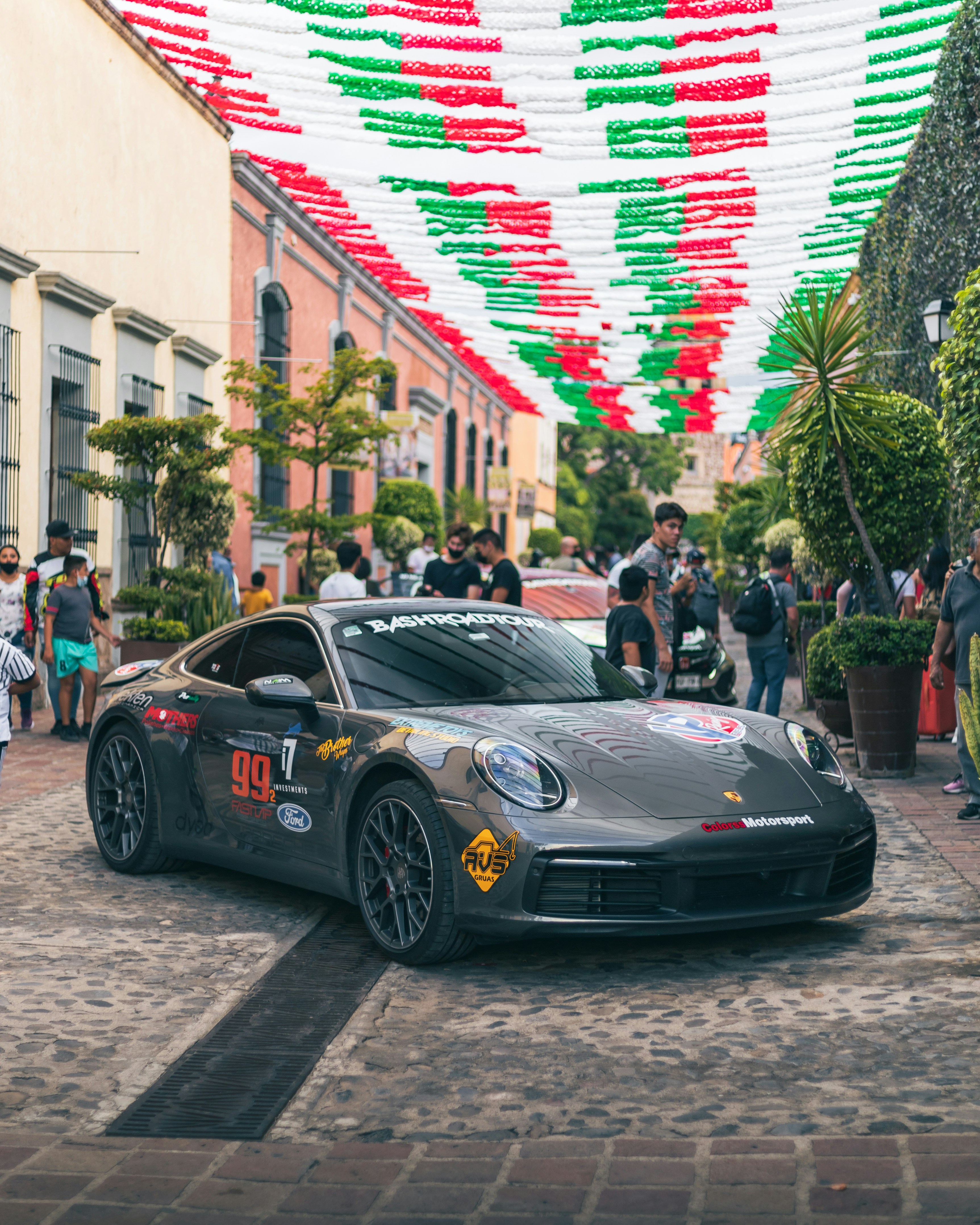 Gray Porsche 911 Pauses on Cobblestones Beneath Festive Red-Green Canopies