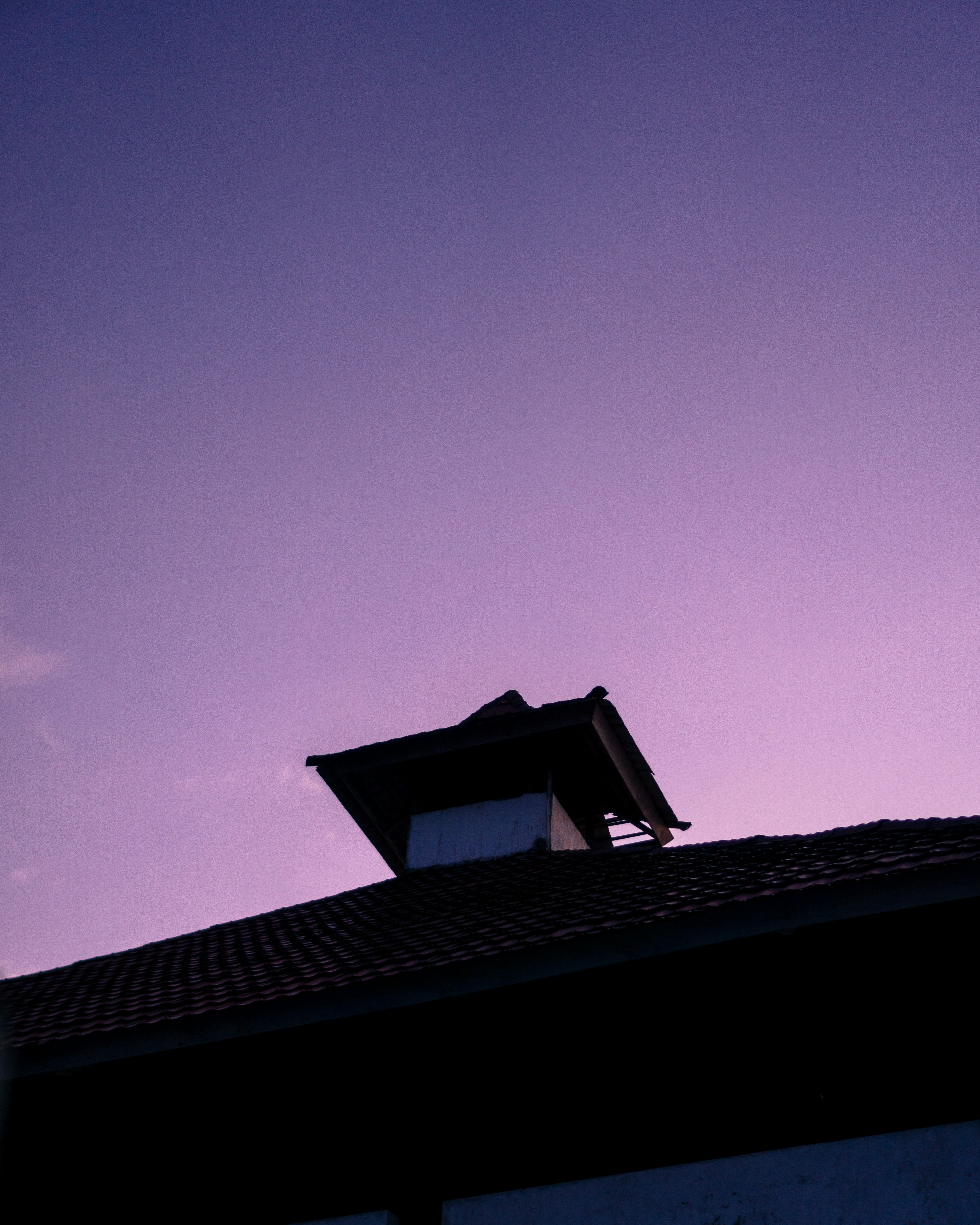 Silhouette of a house rooftop against a gradient twilight sky, showcasing the transition from day to night.