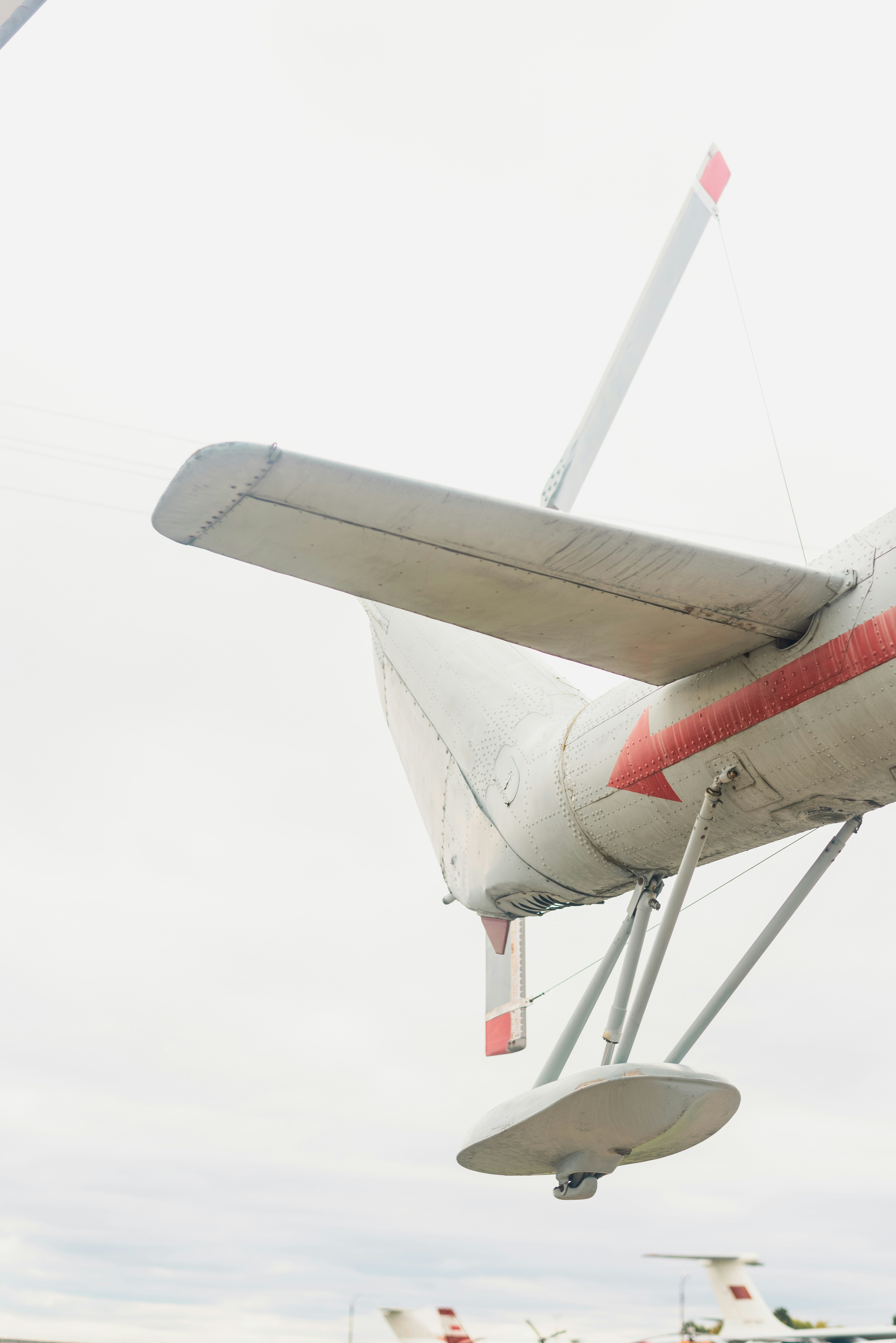 Weathered Seaplane Wing: Close-Up of White Hull and Red Markings Against a Bleached Sky