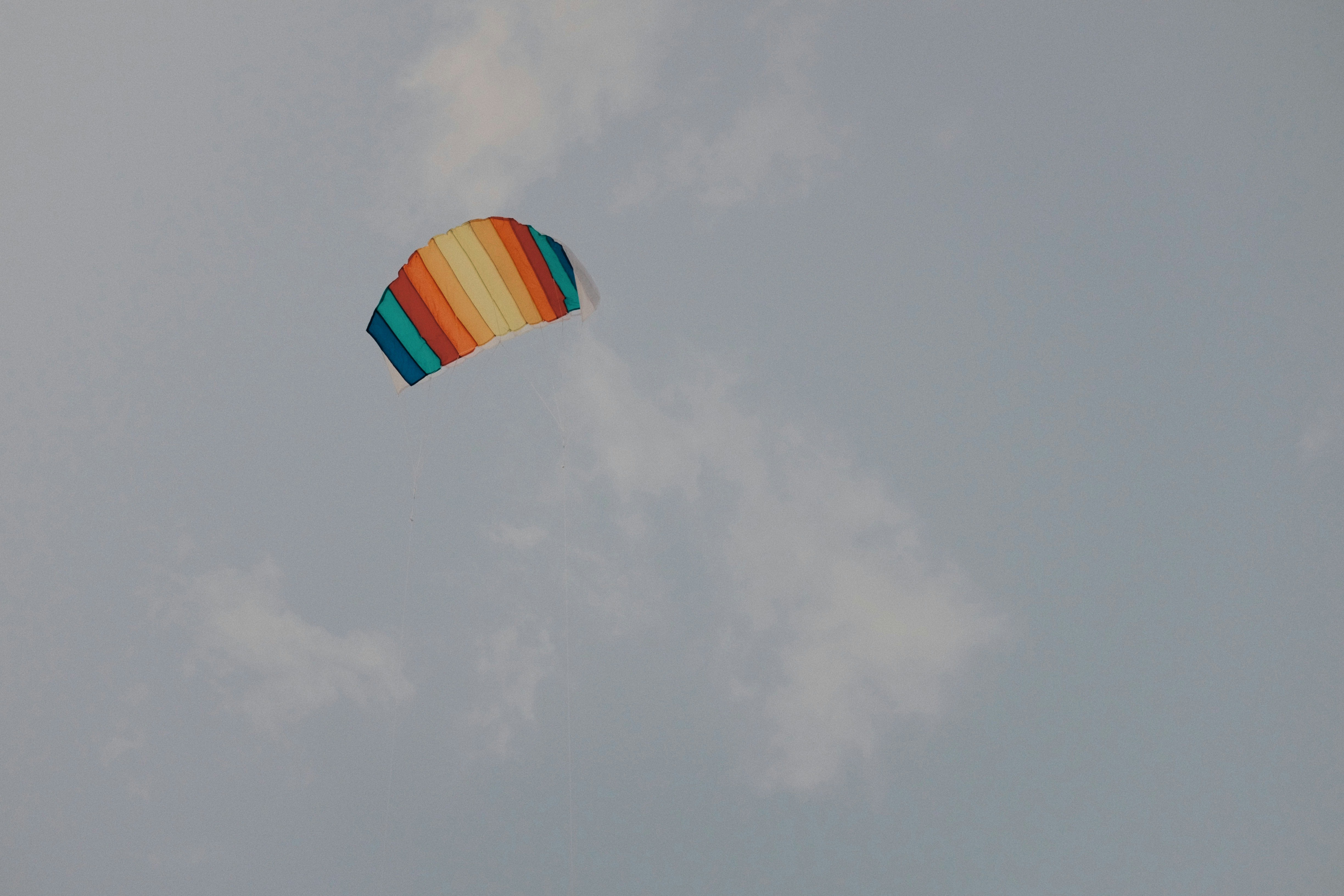 Colorful kite soaring against a backdrop of soft clouds in a clear blue sky.