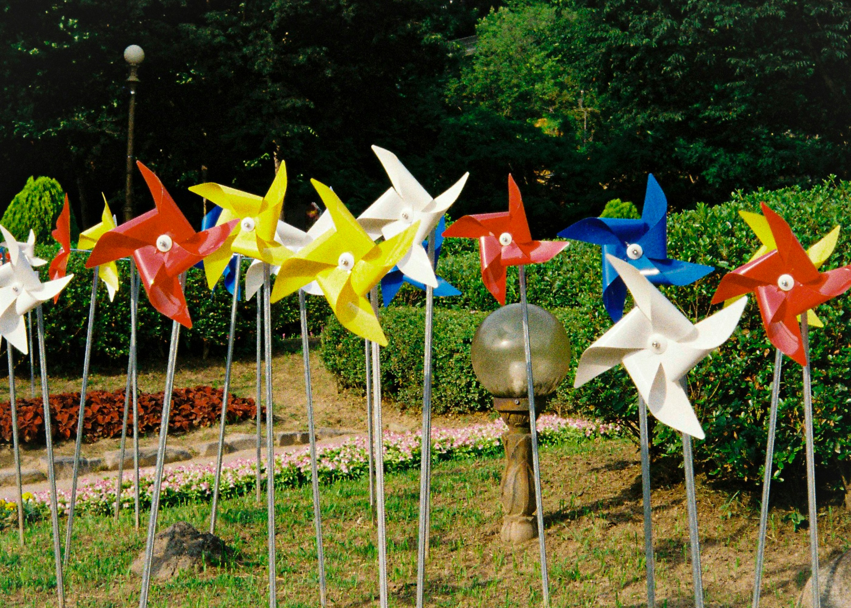 Colorful pinwheels spinning in a garden, surrounded by lush greenery and floral accents. A decorative orb adds a whimsical touch.