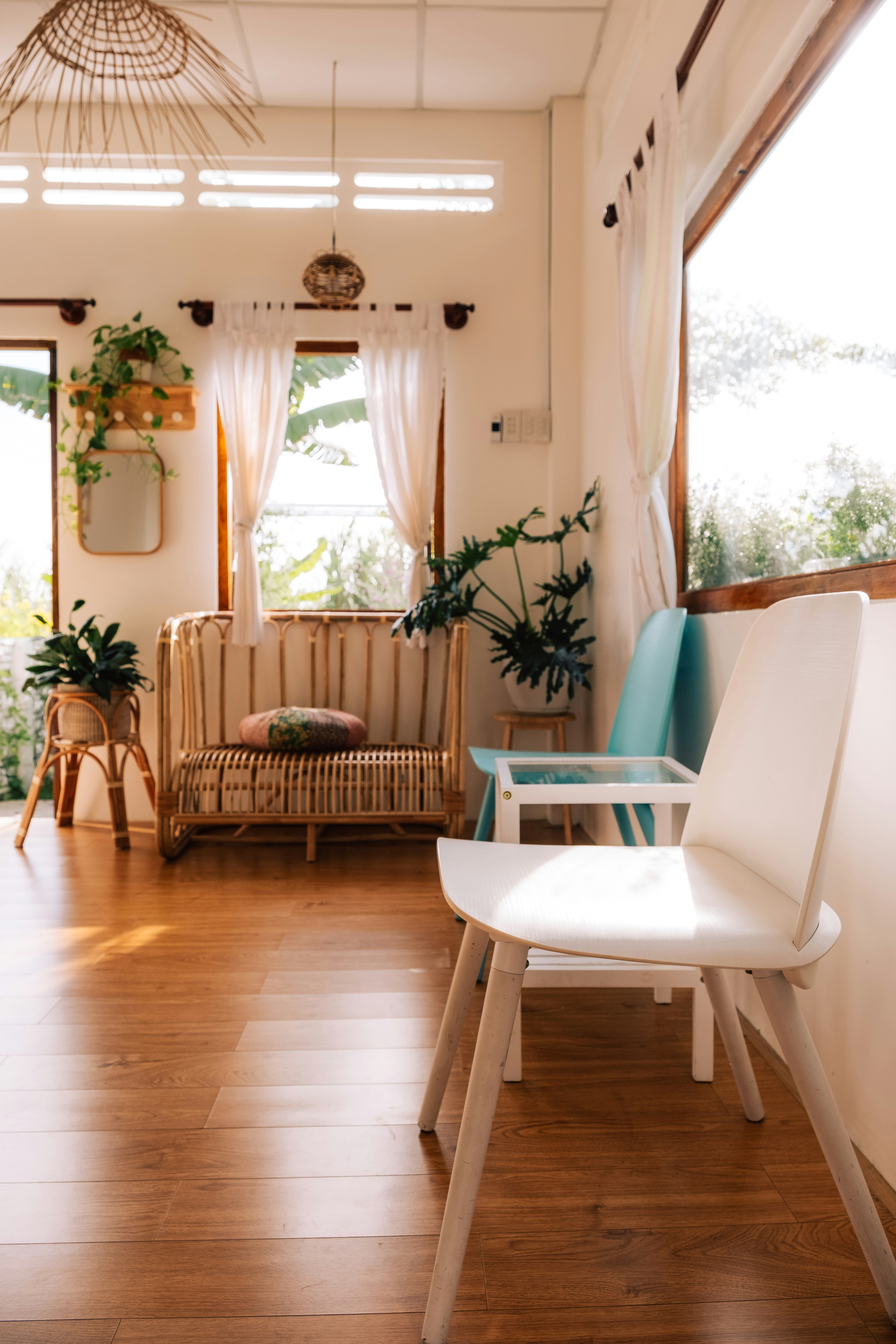 Cozy interior featuring a rattan sofa, potted plants, and a sunlit window, creating a tranquil atmosphere perfect for relaxation.