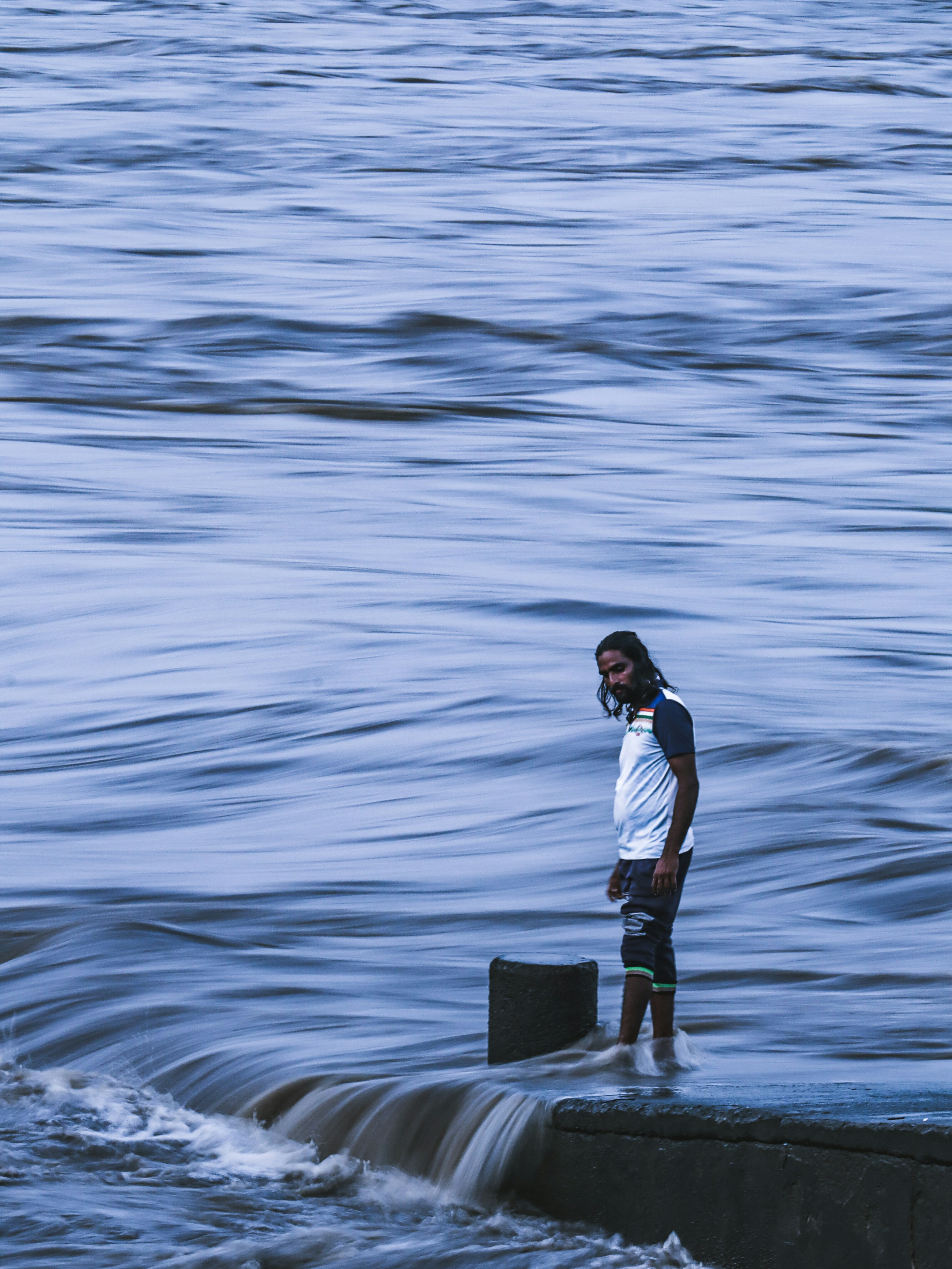 A lone figure stands on a pier, gazing into the turbulent waters, capturing a moment of contemplation amidst nature's chaos.