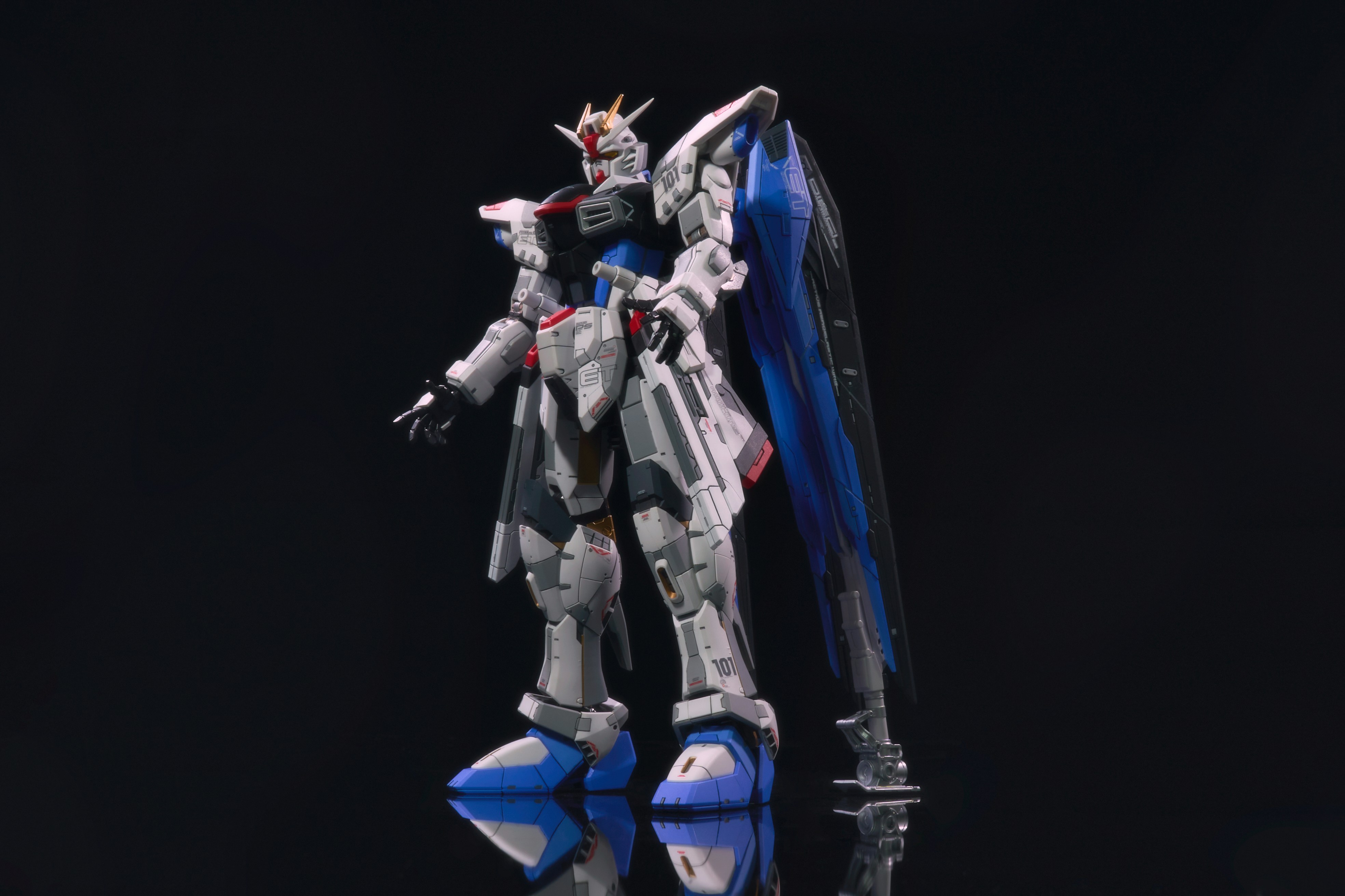 A detailed Gundam model stands confidently against a dark backdrop, showcasing intricate design and craftsmanship. The reflective surface enhances its striking features.