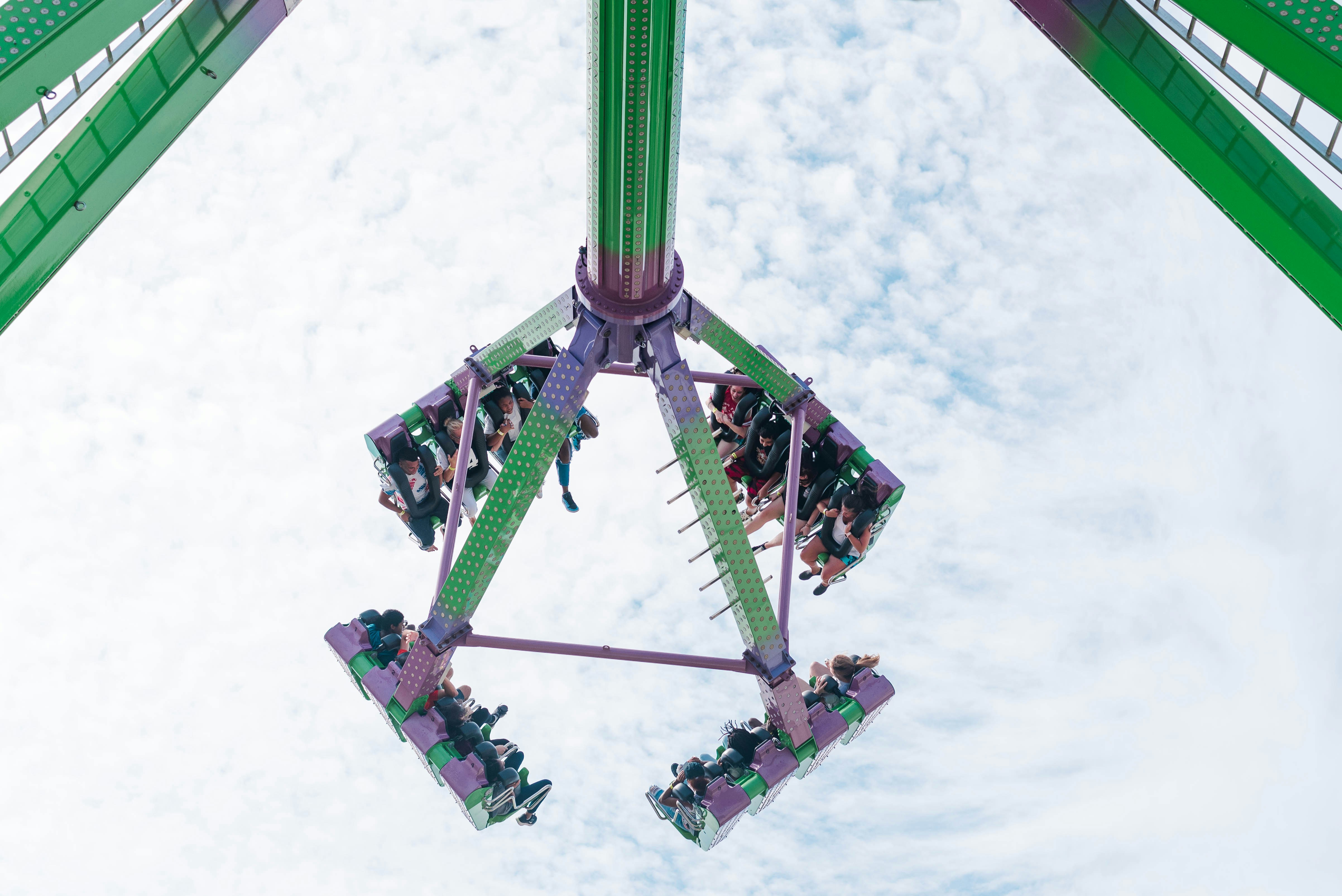 Amusement park ride spins overhead, showcasing exhilarated riders against a backdrop of cloudy sky.