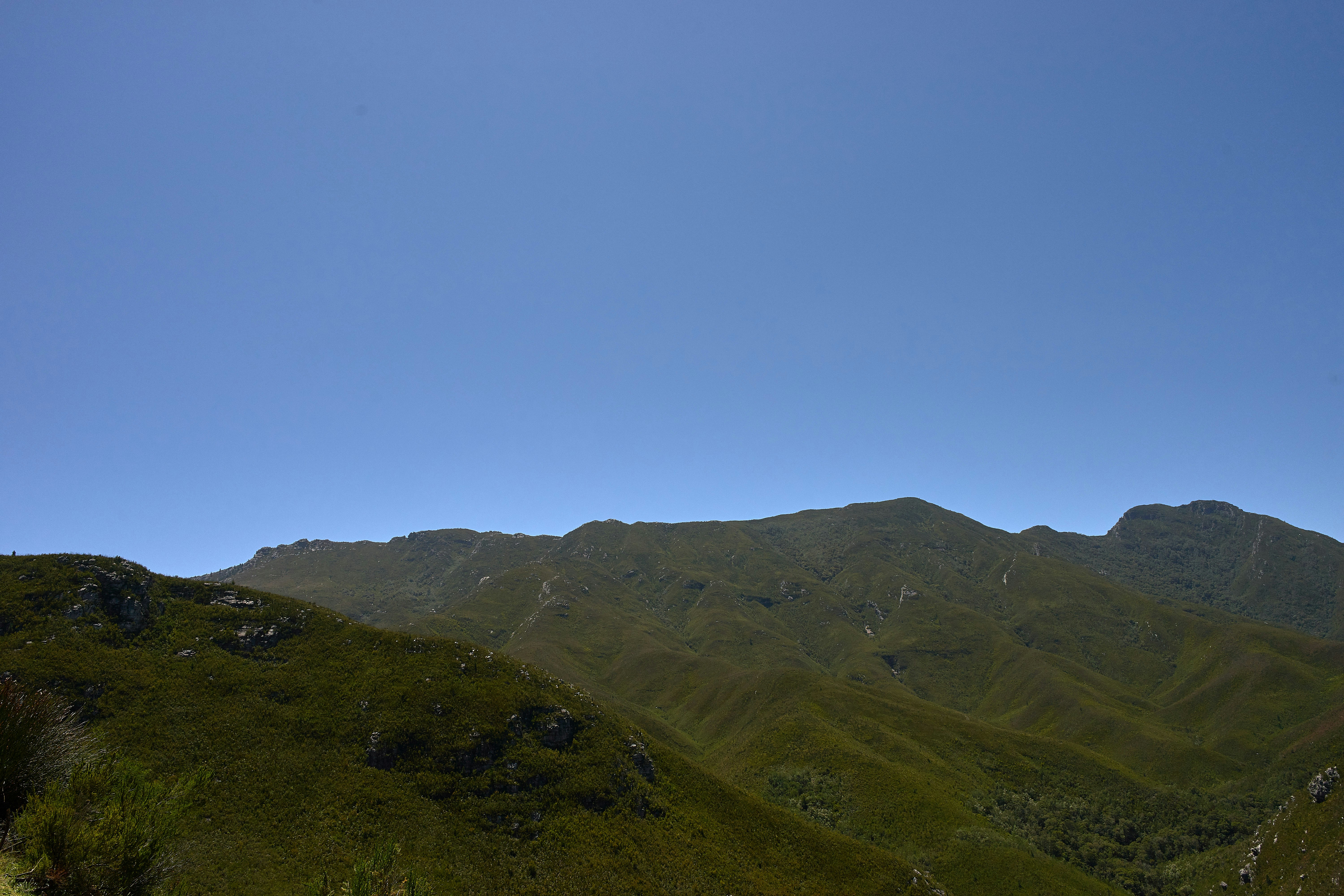 Expansive view of lush green mountains under a clear blue sky, showcasing the natural beauty of the landscape.