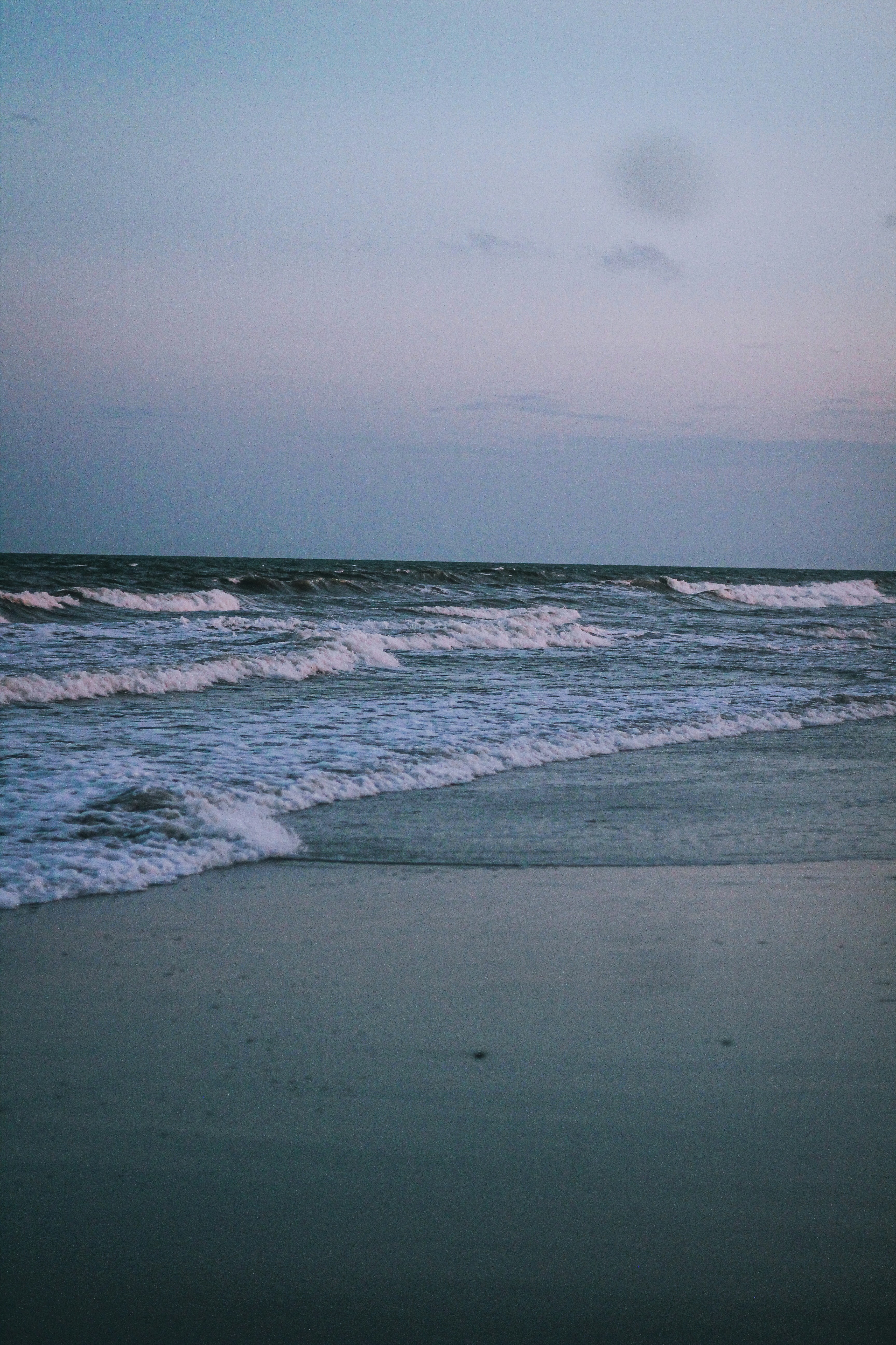 Gentle waves rolling onto a serene beach under a twilight sky, creating a tranquil atmosphere.